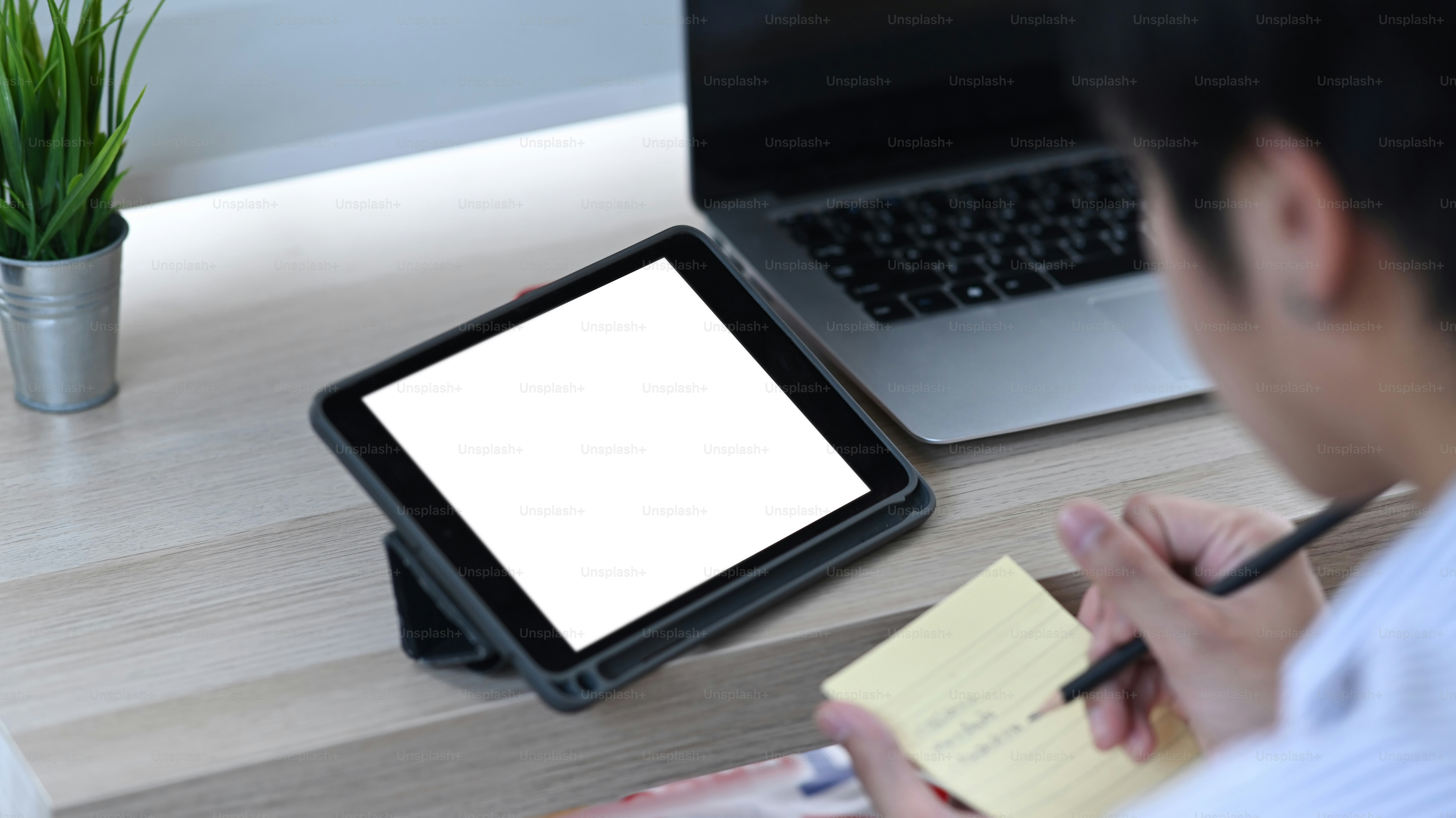 A designer man is taking note on notebook while looking information in ...