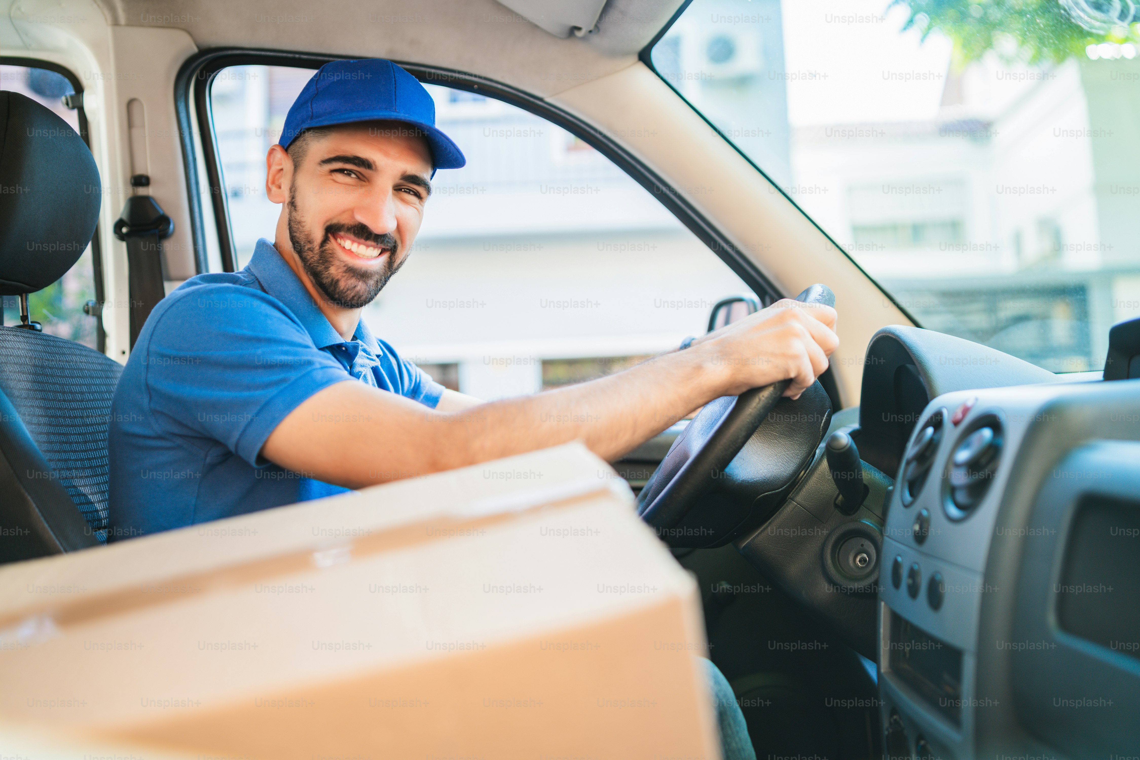 Portrait of a delivery man driver driving van with cardboard boxes on ...
