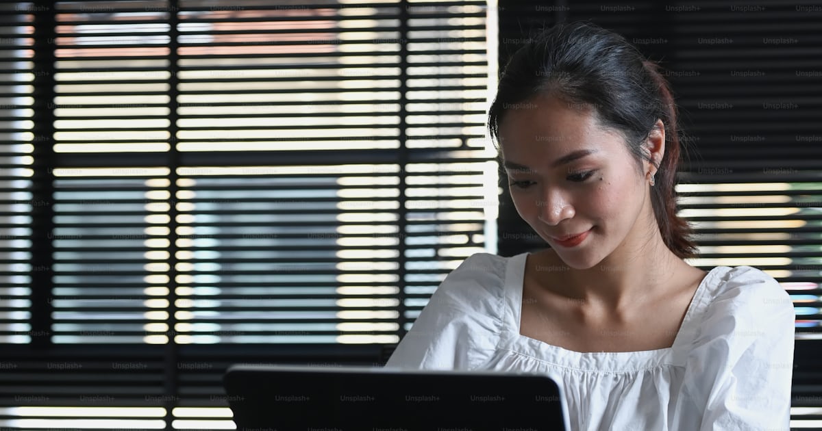 現代のオフィスに座りながらコンピューターのタブレットを使用する笑顔の女性。の写真 Unsplashのオフィスの画像
