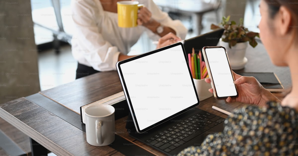創造的なデザイナーの女性がタブレットで作業し、スマートフォンを使用しています。グラフィック表示モンタージュ用の空白の画面。の写真 テーブル