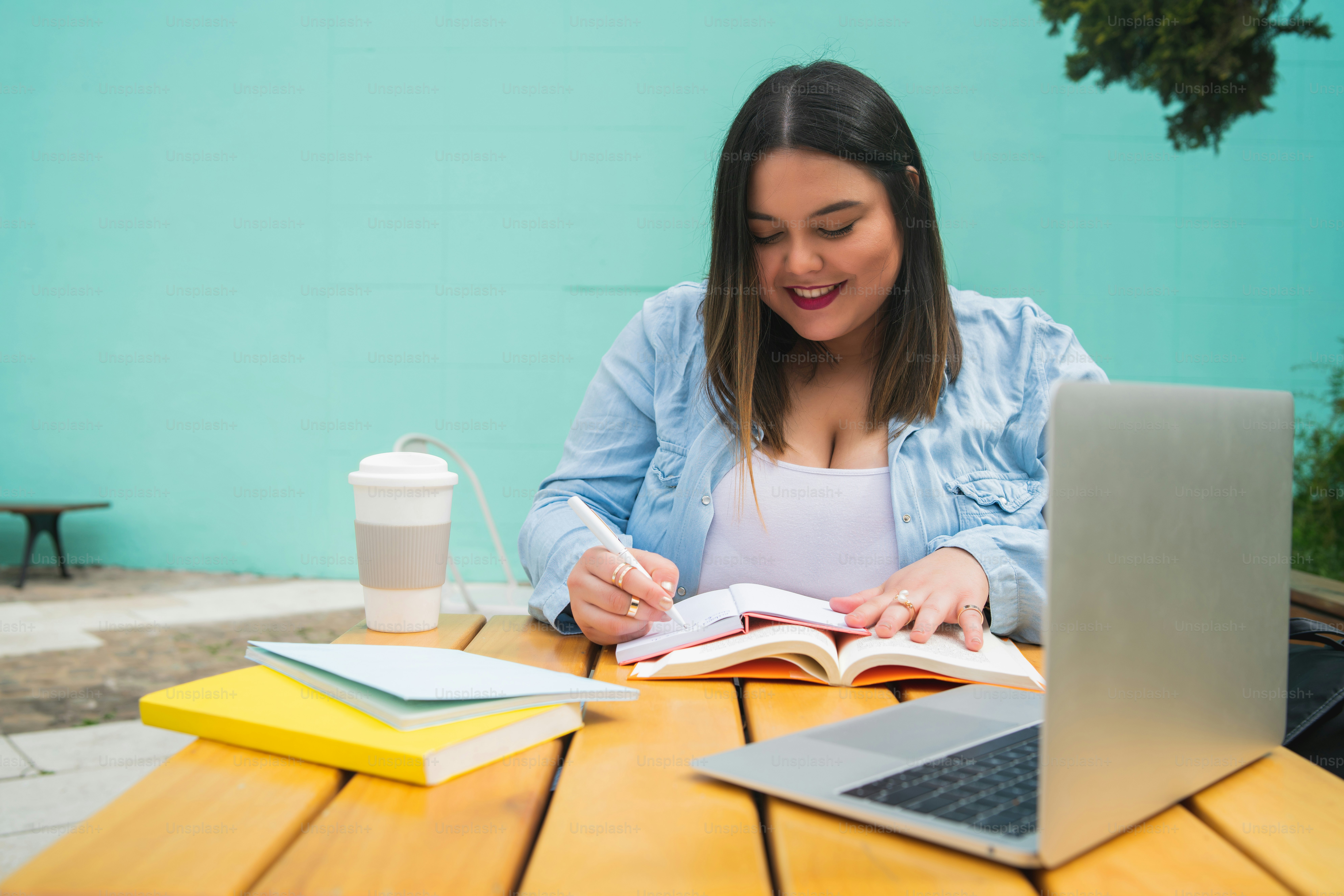 Portrait of young pluse size woman studying with laptop and books while ...