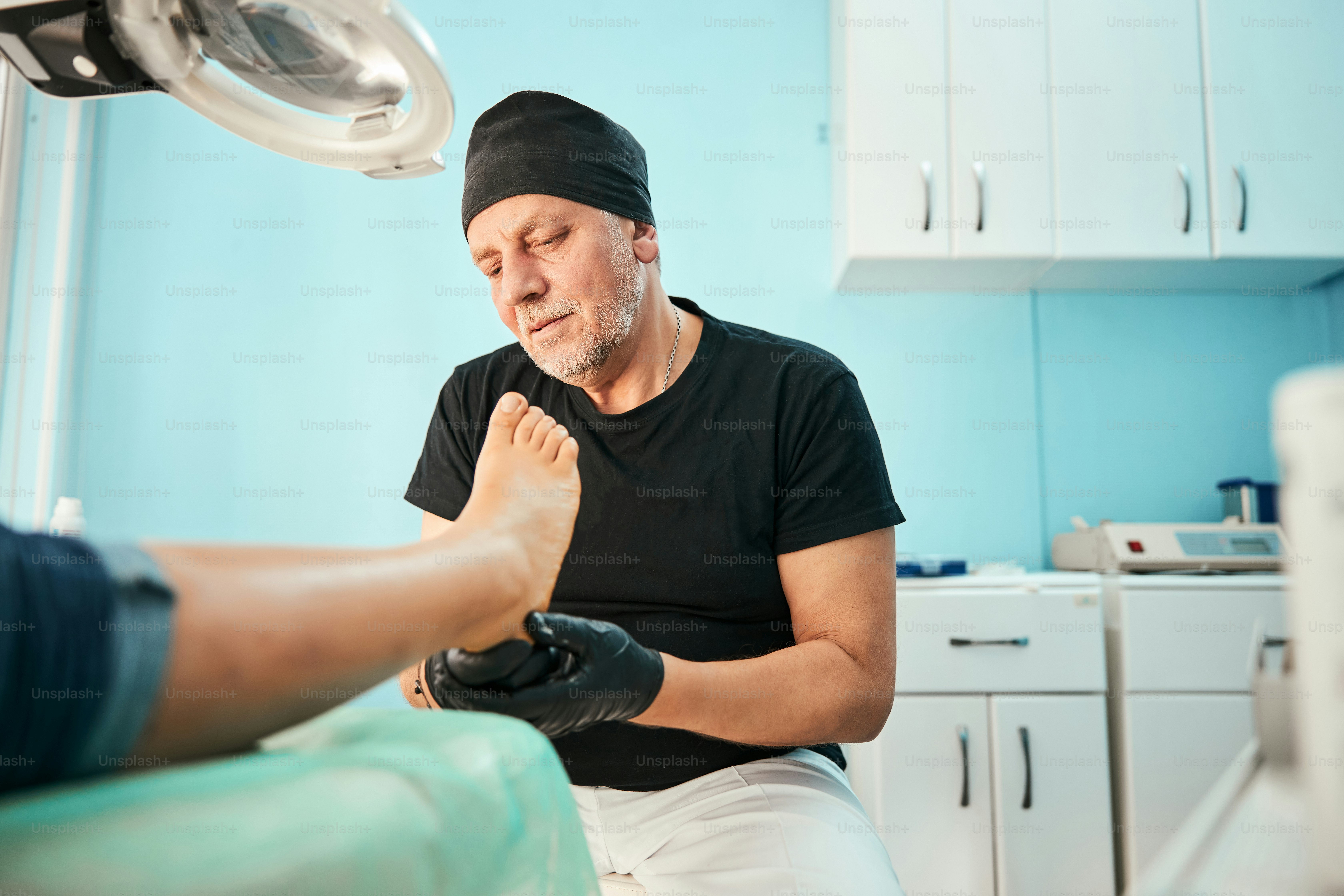 Podólogo atento sentado en su lugar de trabajo mientras va a tratar un ...