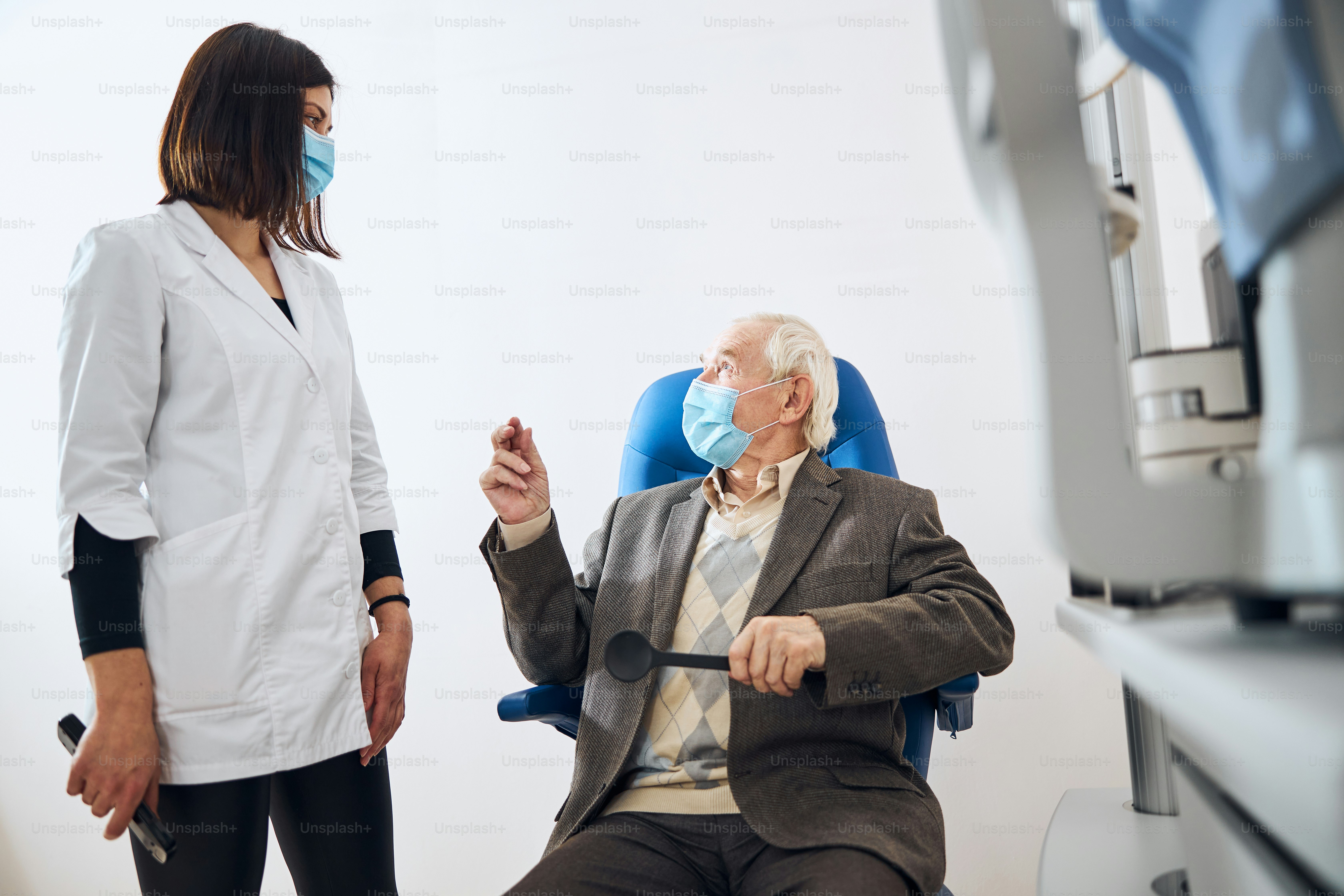 Gray-headed man with an occluder in his hand talking to an optometrist ...