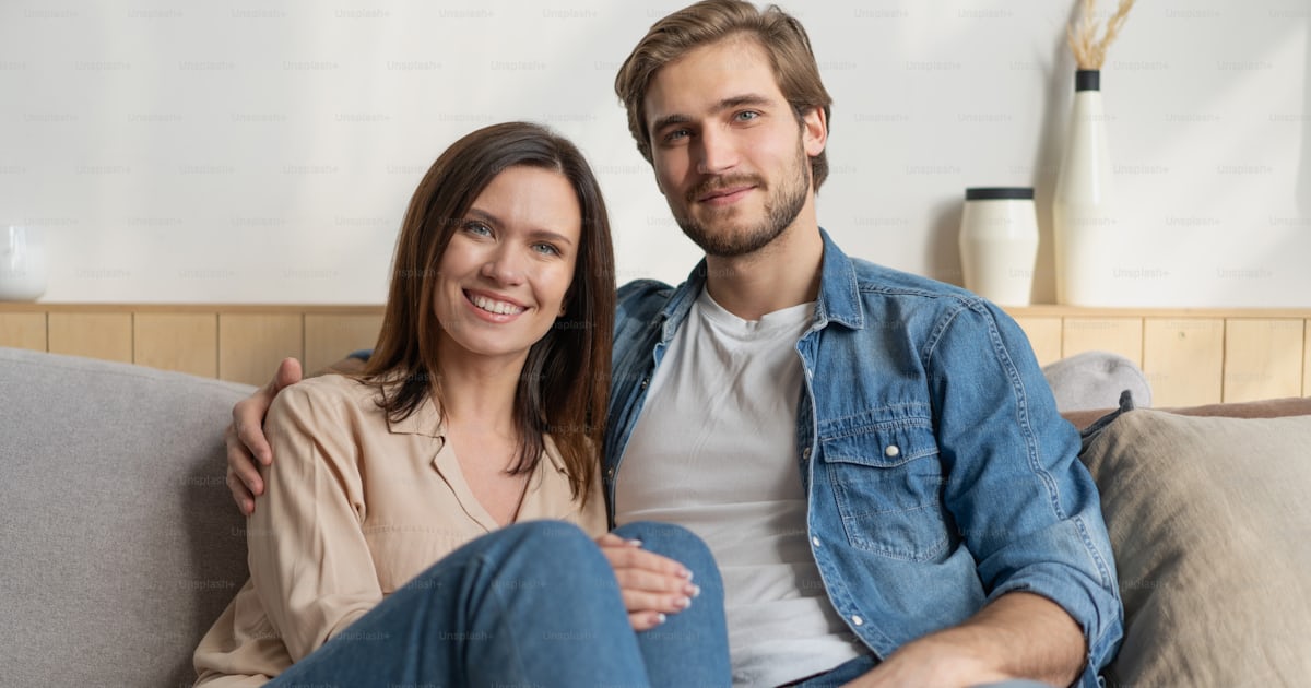 幸せな若い白人夫婦は、自宅の居心地の良いソファでリラックスし、遠くを見て一緒に夢を見、夢のようなミレニアル世代の男性と女性が快適なソファで