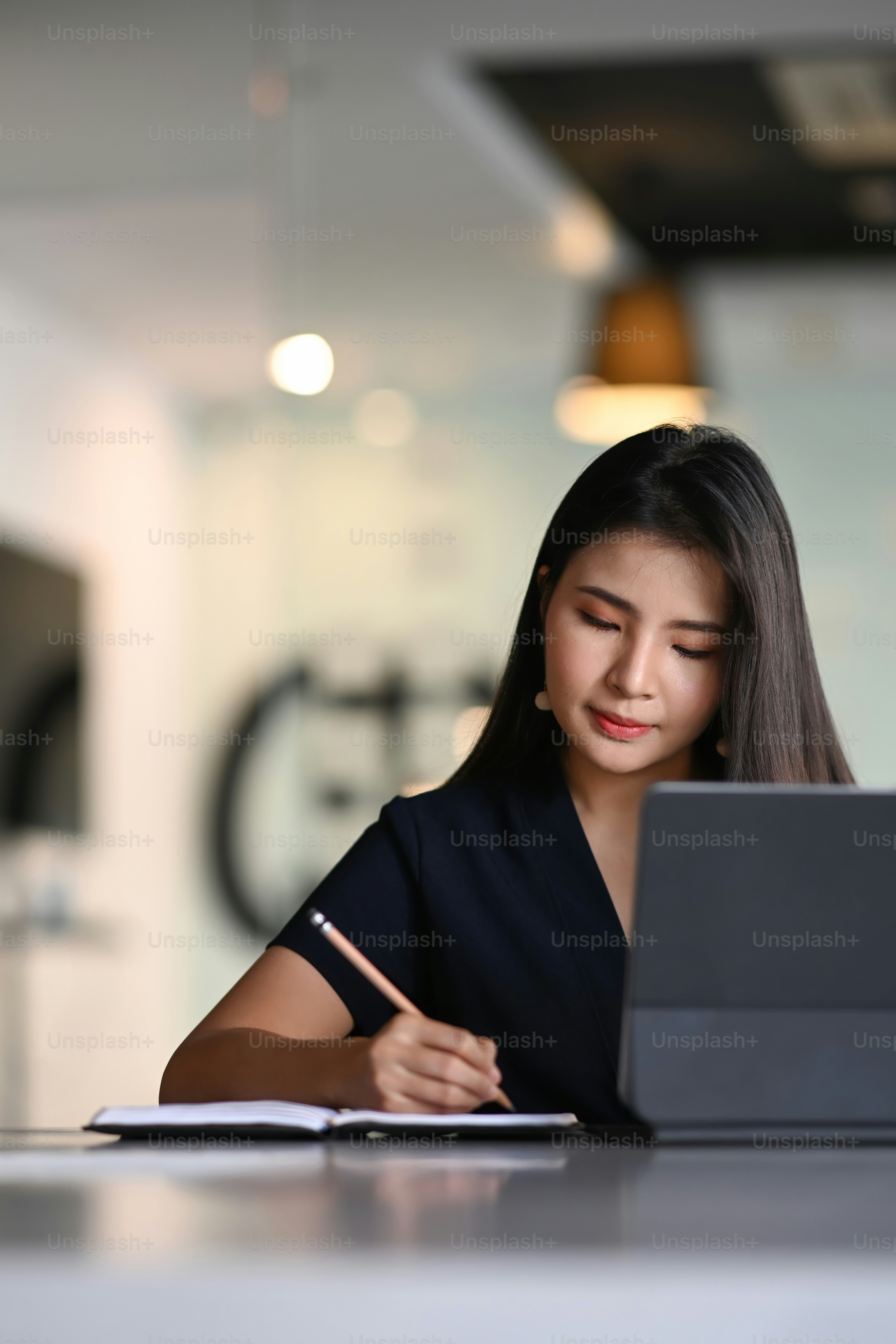 Retrato de una mujer de negocios usando una tableta y escribiendo información en un cuaderno ...