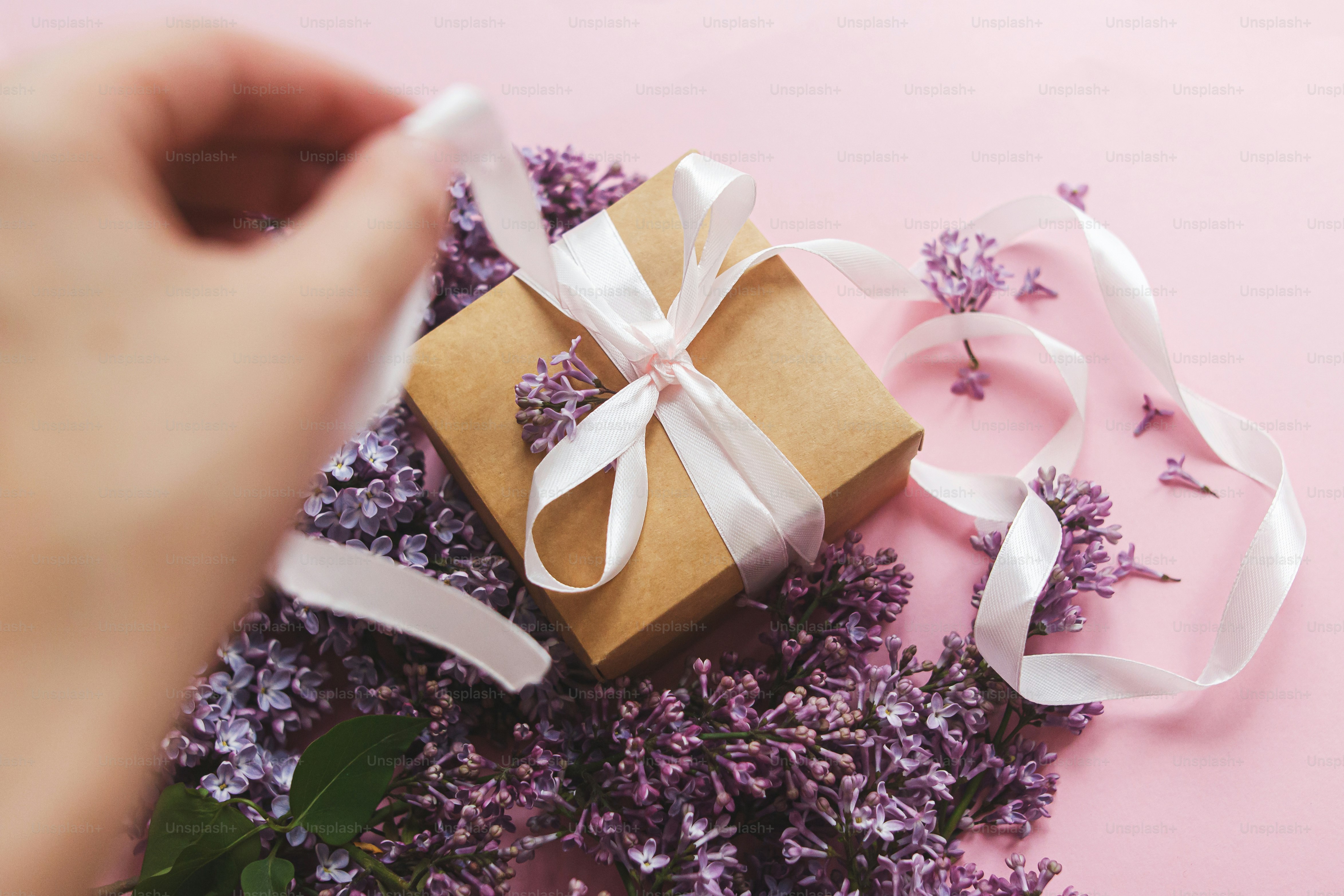 Hand opening gift box with ribbon and lilac flowers on pink paper, view ...