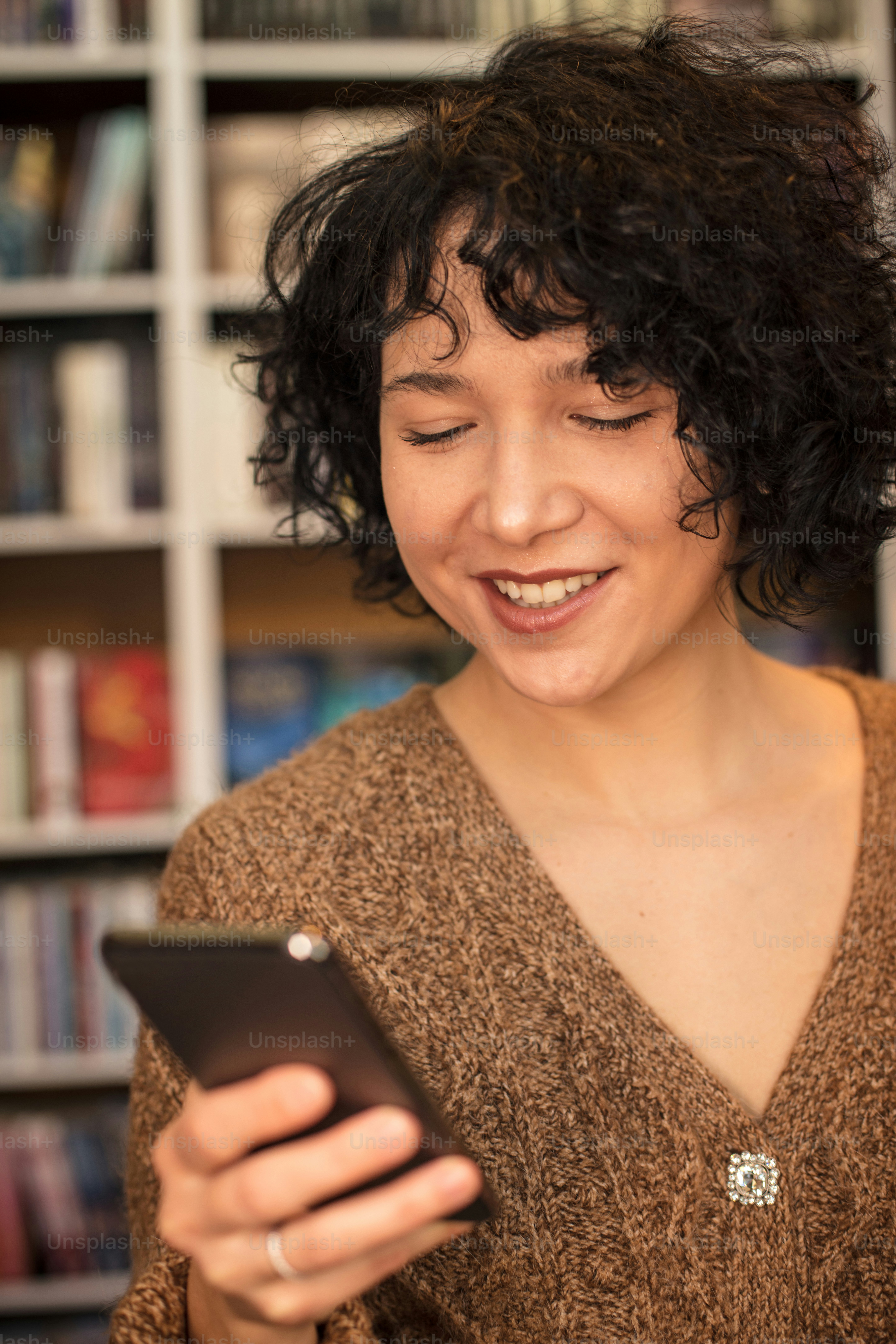 Femme souriante dans la bibliothèque utilisant un téléphone intelligent ...