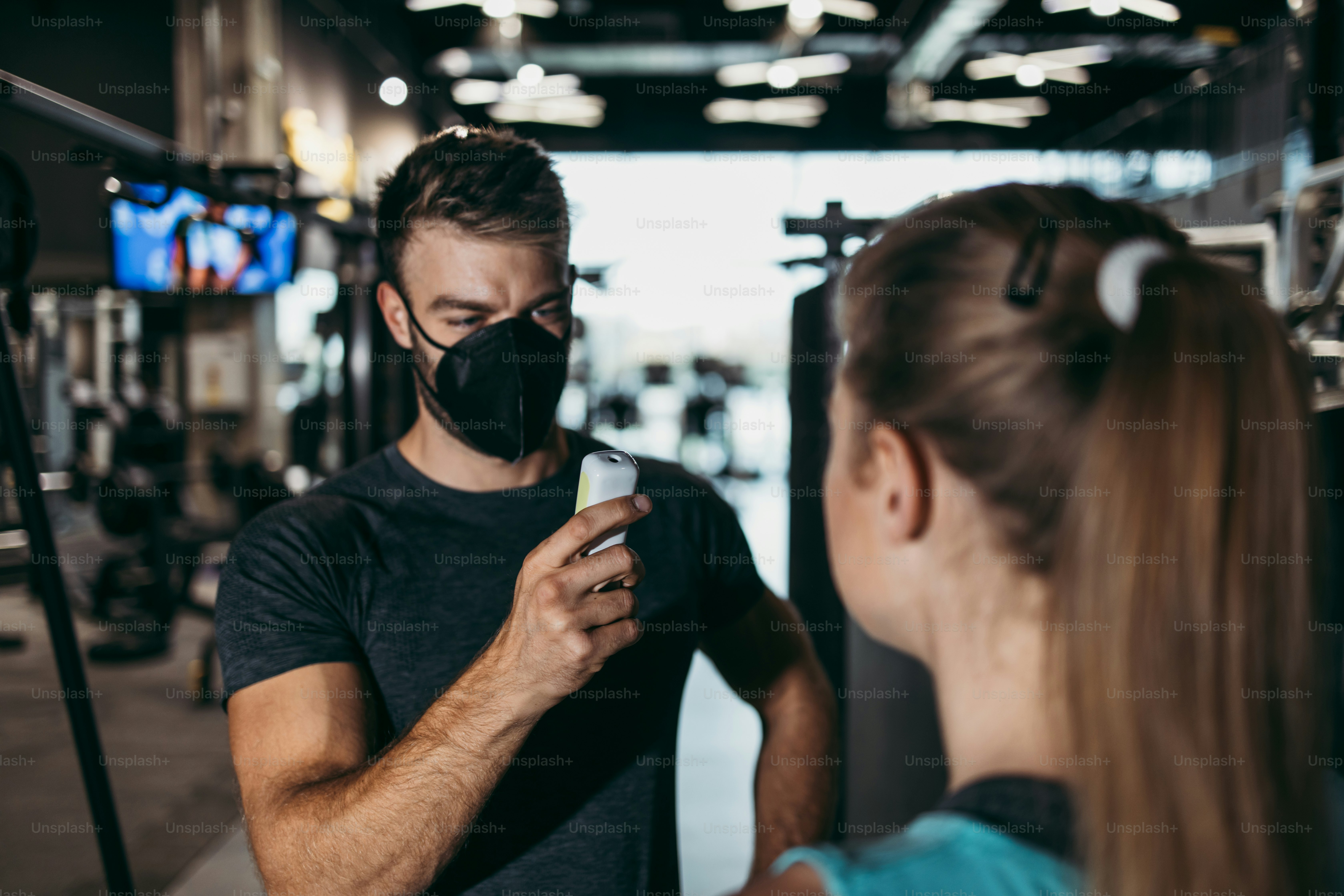 Young male fitness gym worker and instructor measuring body temperature ...