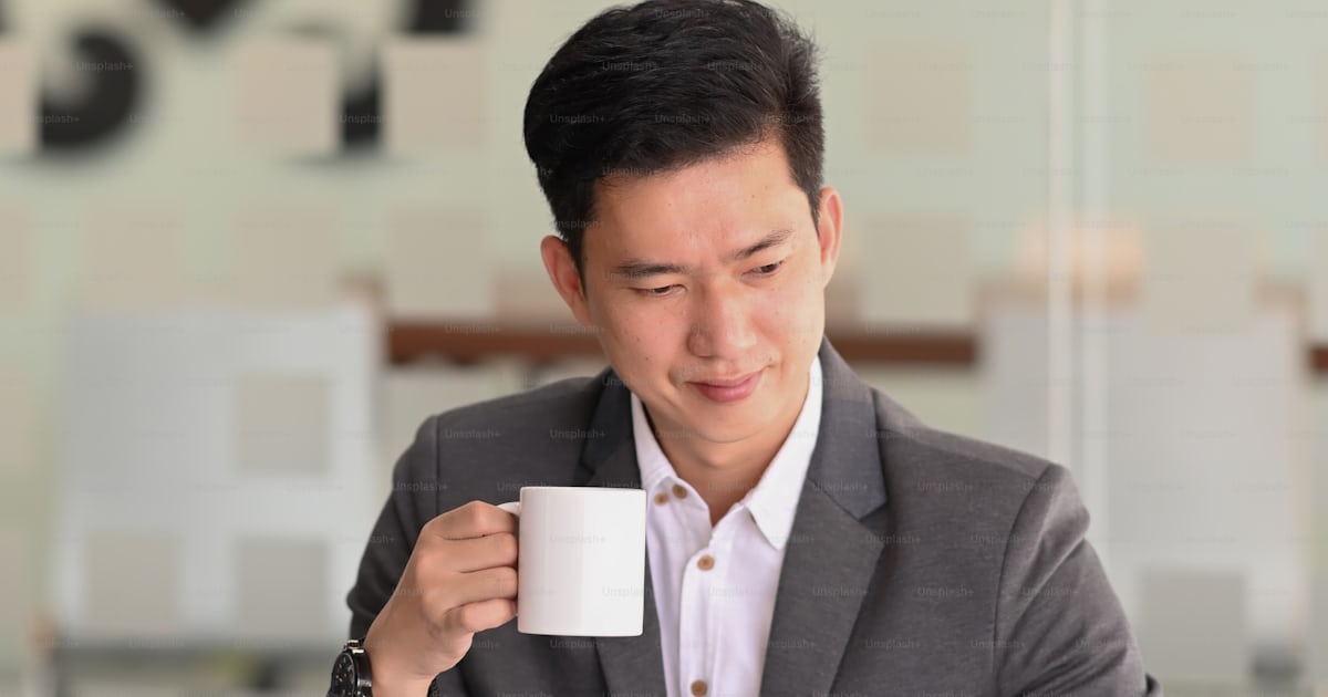 커피 컵을 들고 현대 사무실에서 노트북 컴퓨터의 온라인 정보를 스크롤하는 똑똑한 사업가의 초상화 사진 Unsplash의