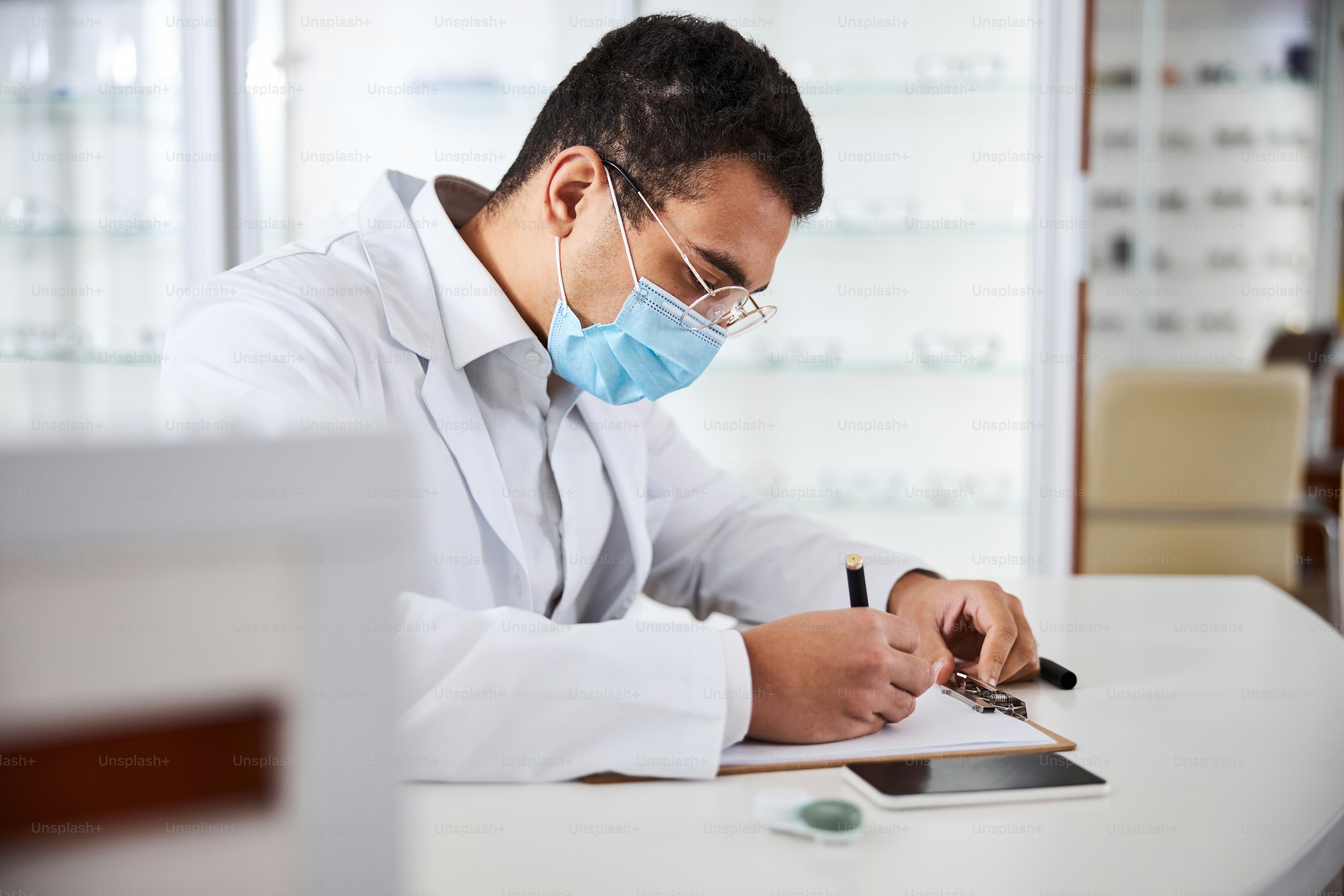 Side view of a focused male optician writing with a pen on a sheet of ...