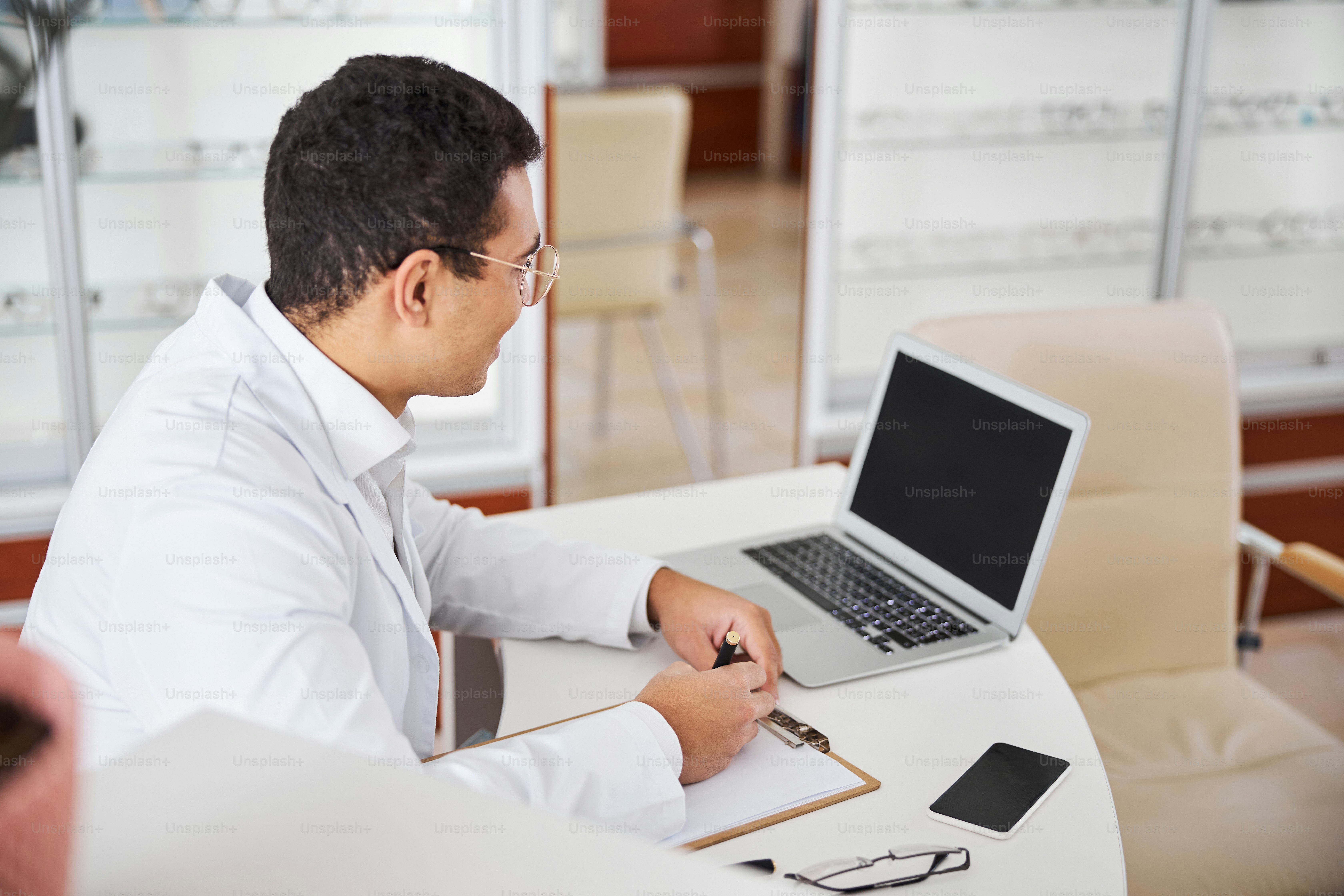 Side view of a bespectacled professional eye doctor writing an eyeglass ...