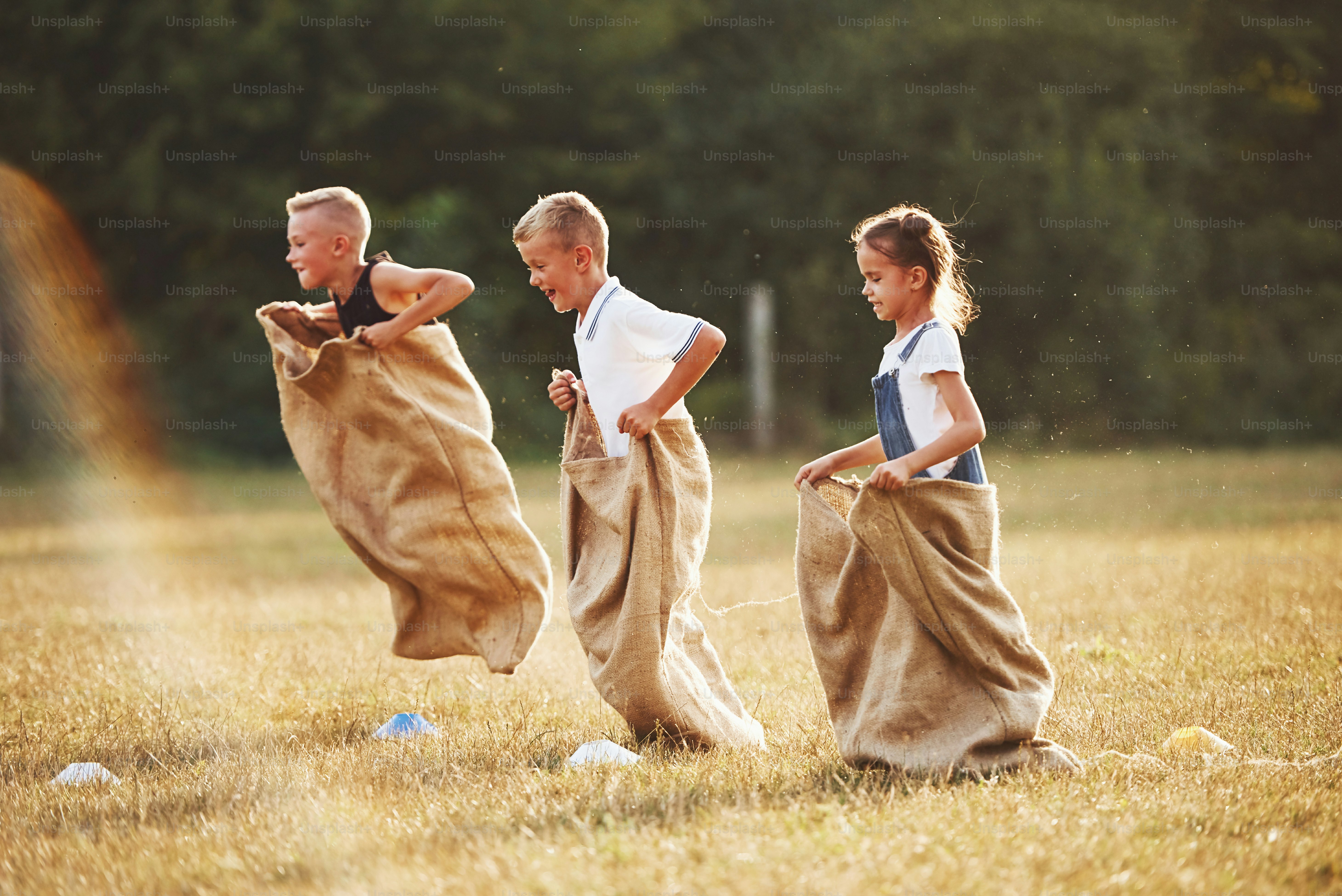 Jumping sack race outdoors in the field. Kids have fun at sunny daytime ...