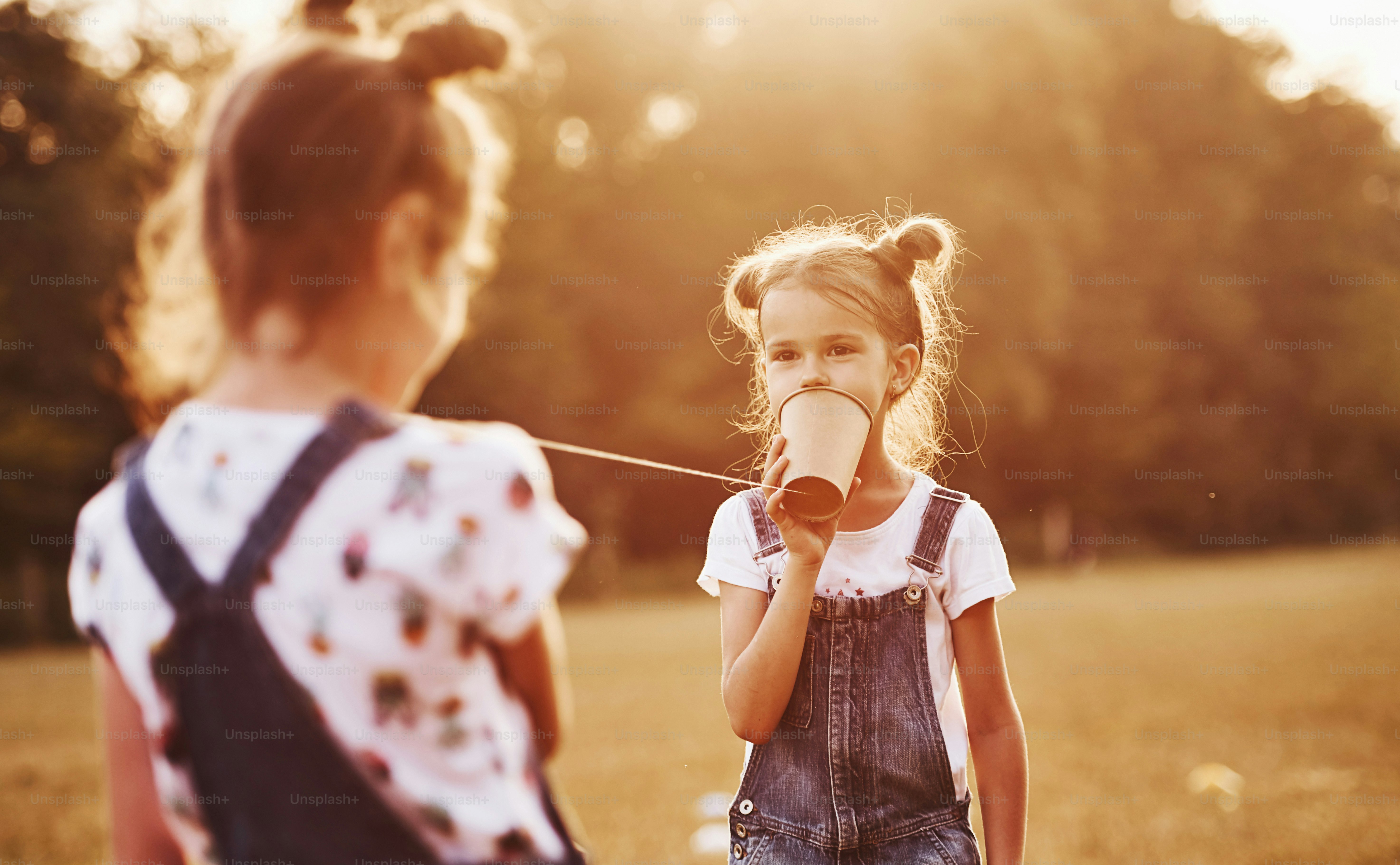 Two female kids stands in the field and talking by using string can ...