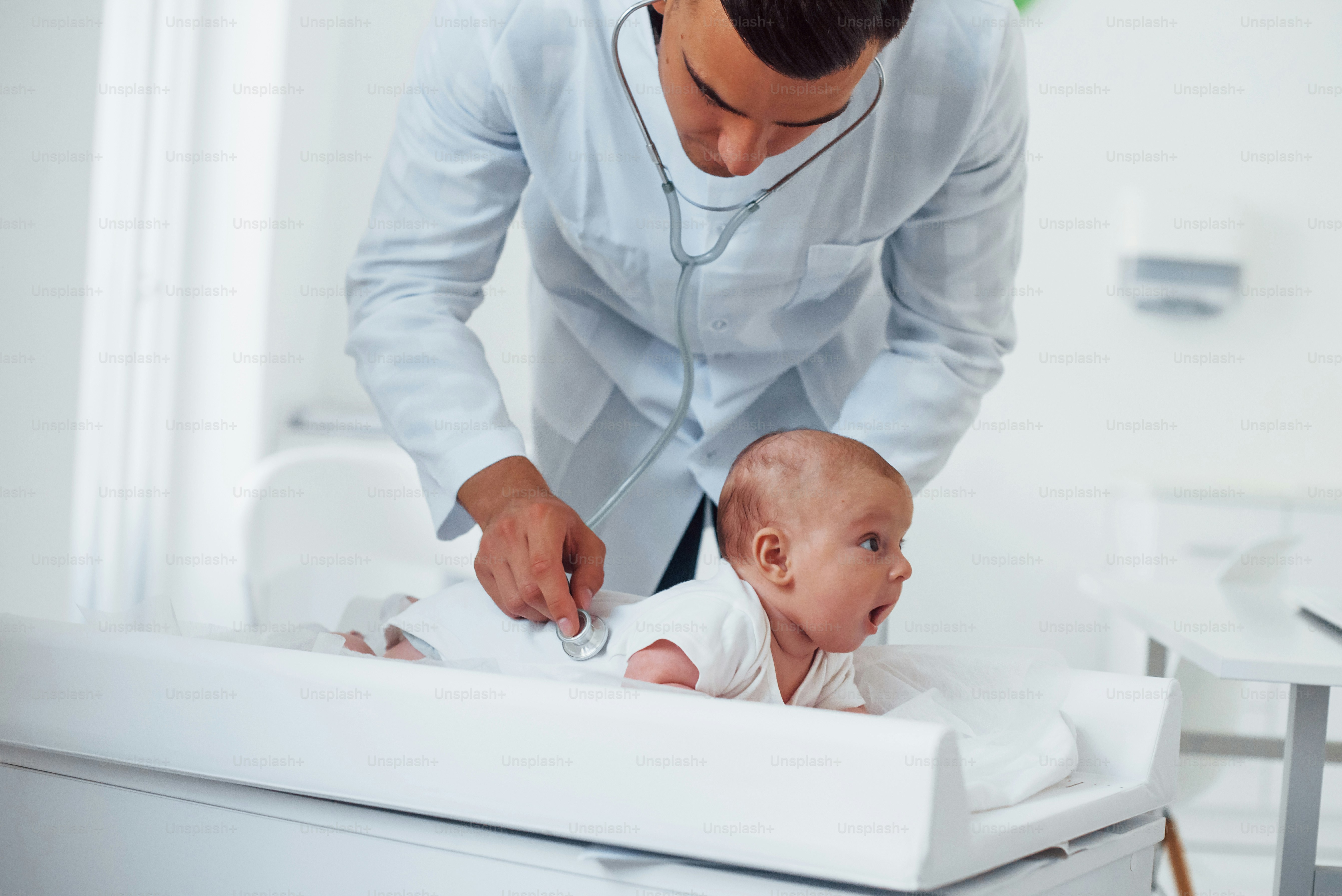 Young pediatrician is with little baby in the clinic at daytime. photo ...