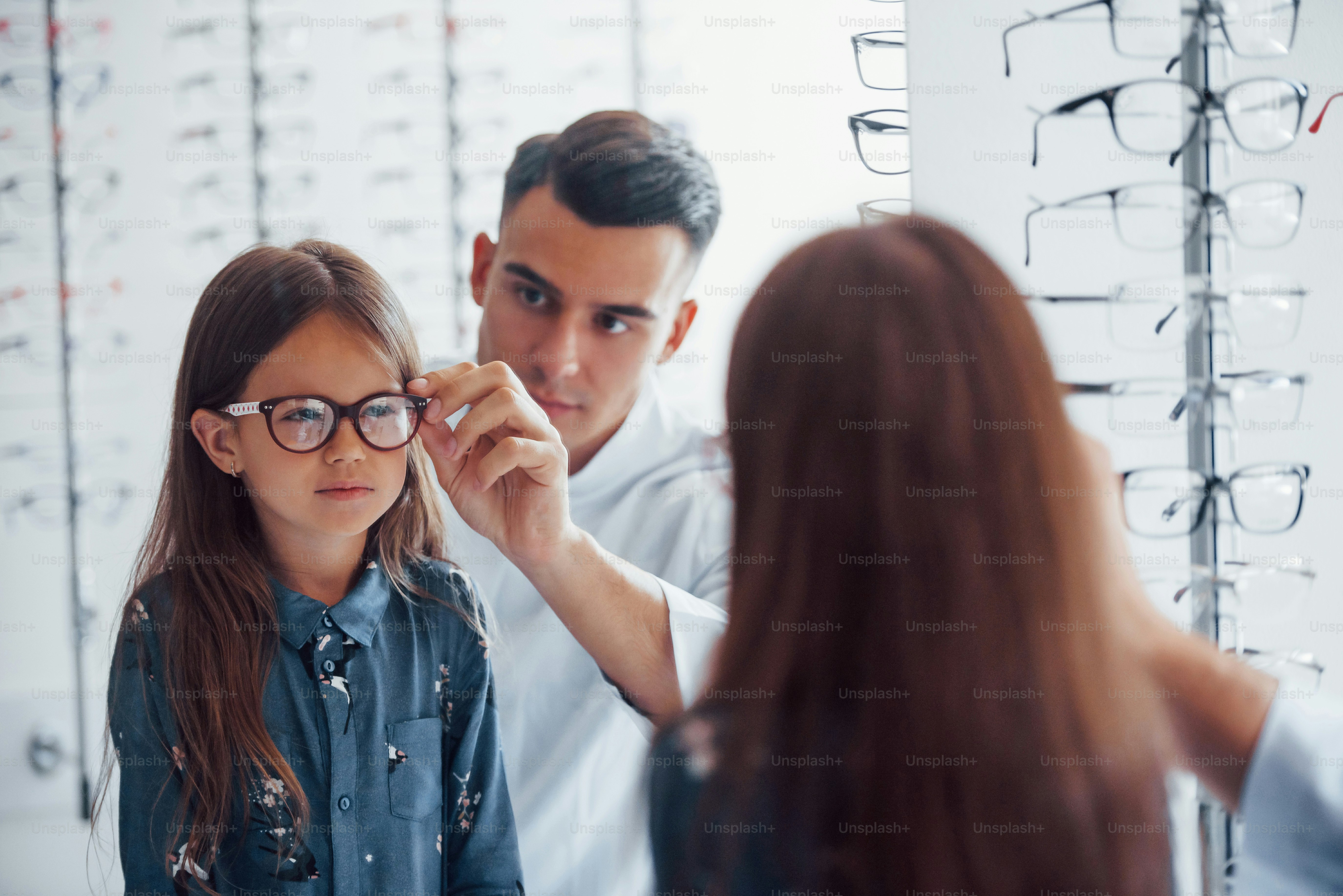 Young pediatrician in white coat helps to get new glasses for little ...
