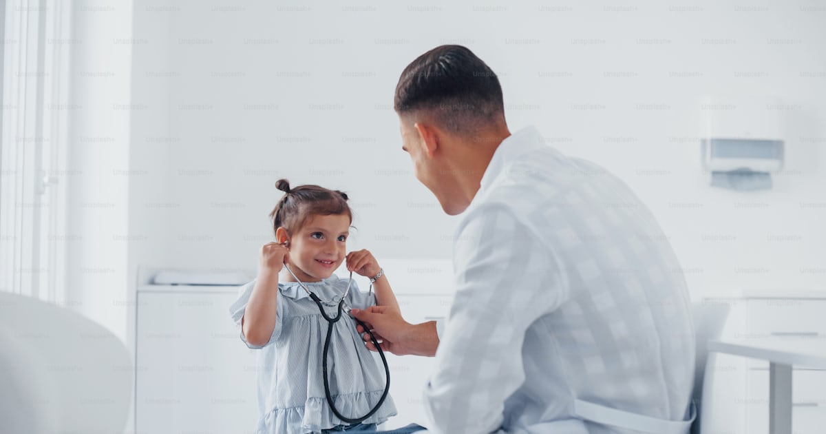 聴診器の使い方を女の子に教えます。若い小児科医は、クリニックで小さな女性の訪問者と一緒に働いています。の写真 ウクライナ Unsplashの写真