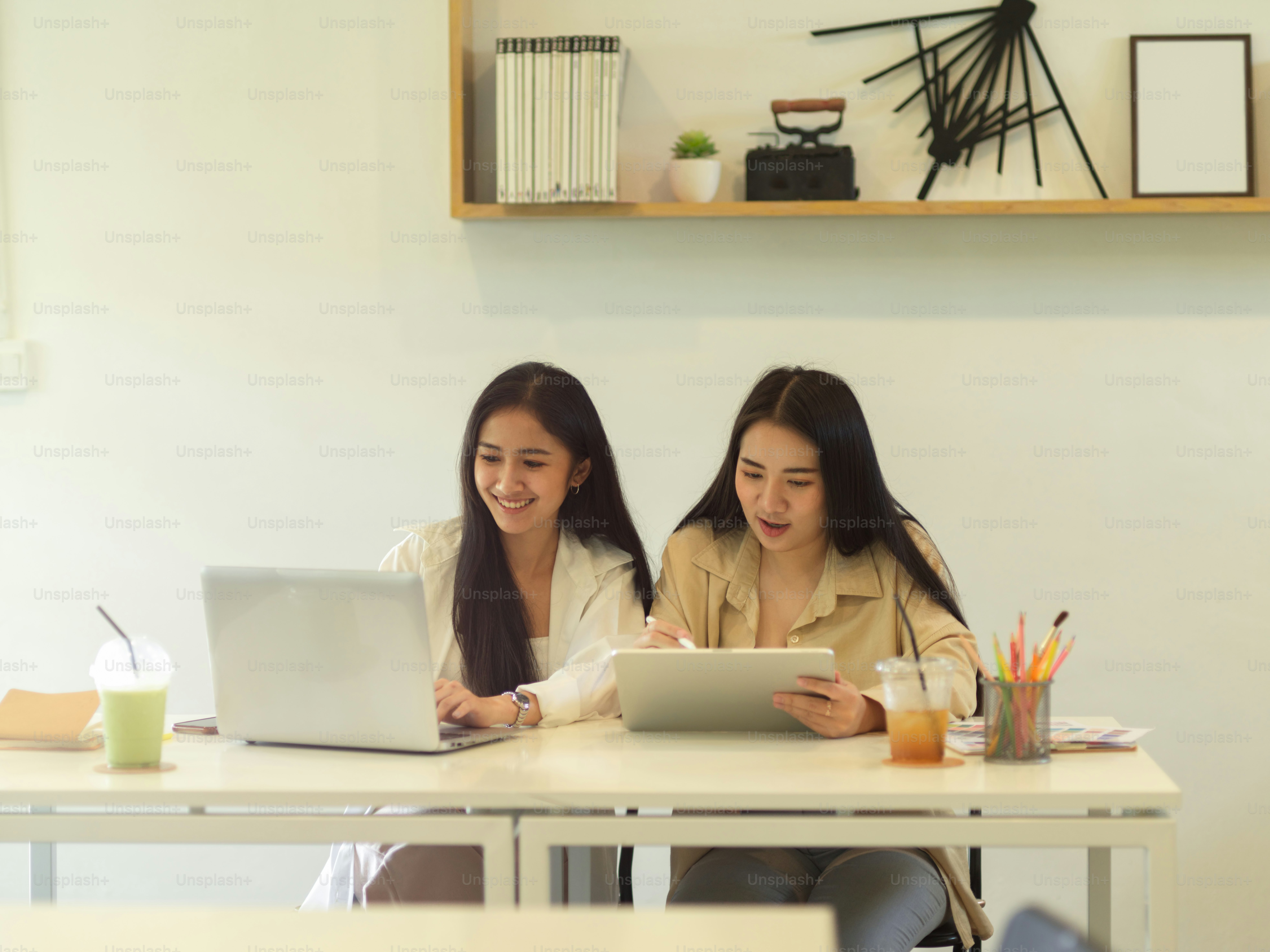Portraits of two female students using tablet and laptop while doing ...