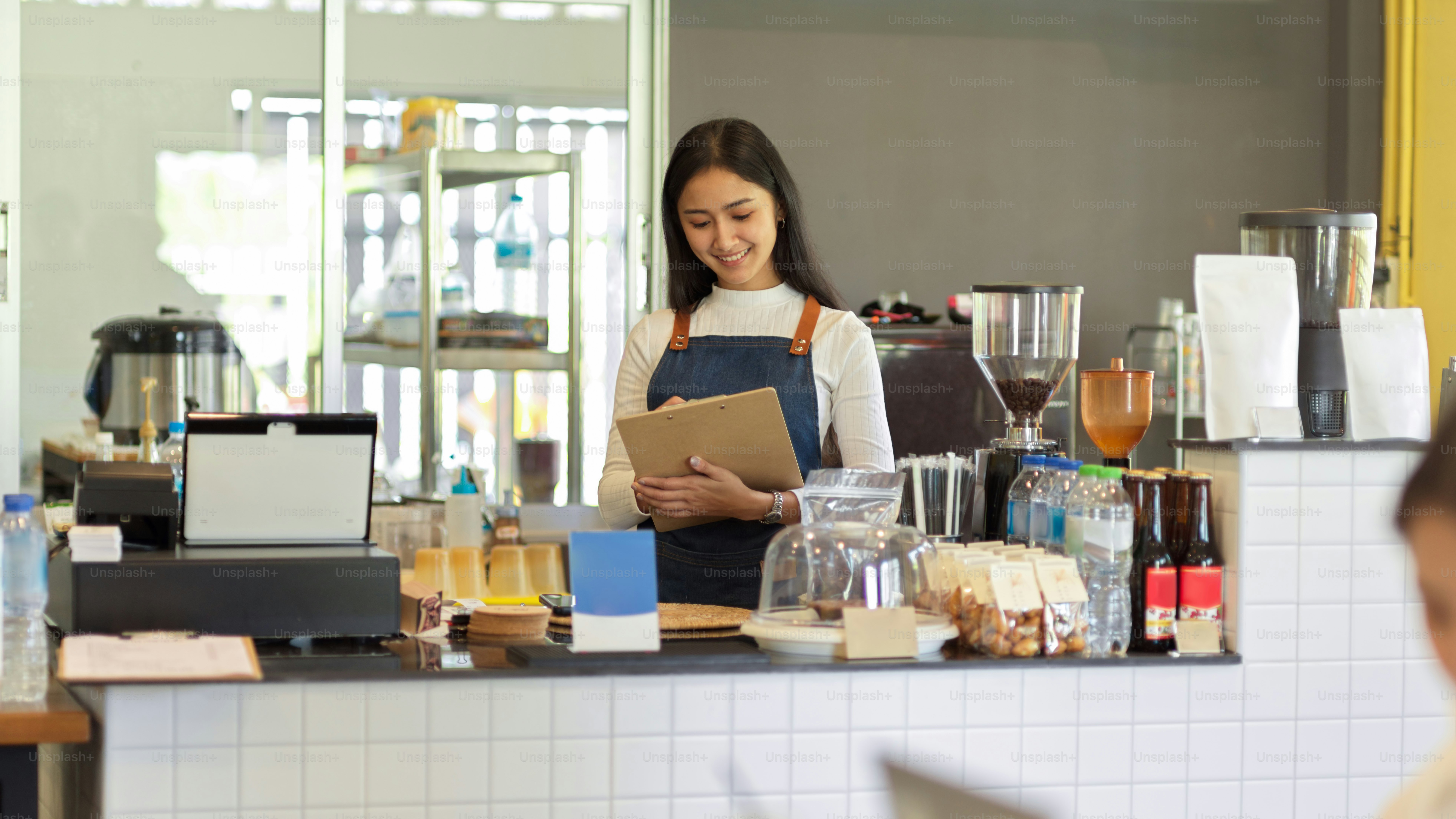 Jeune belle barista avec tablier écrivant une commande tout en se ...