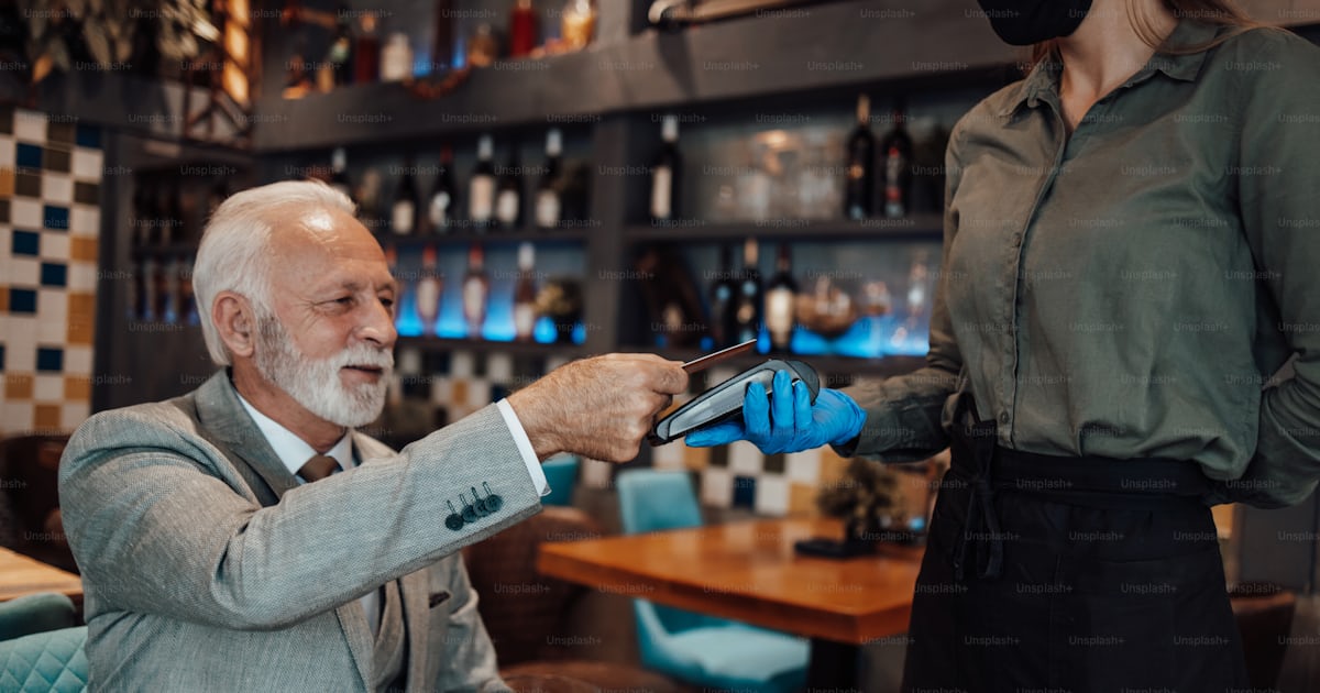 Waitress serves senior gentleman. She holds a card reader while ... Waitress serves senior gentleman. She holds a card reader while ...