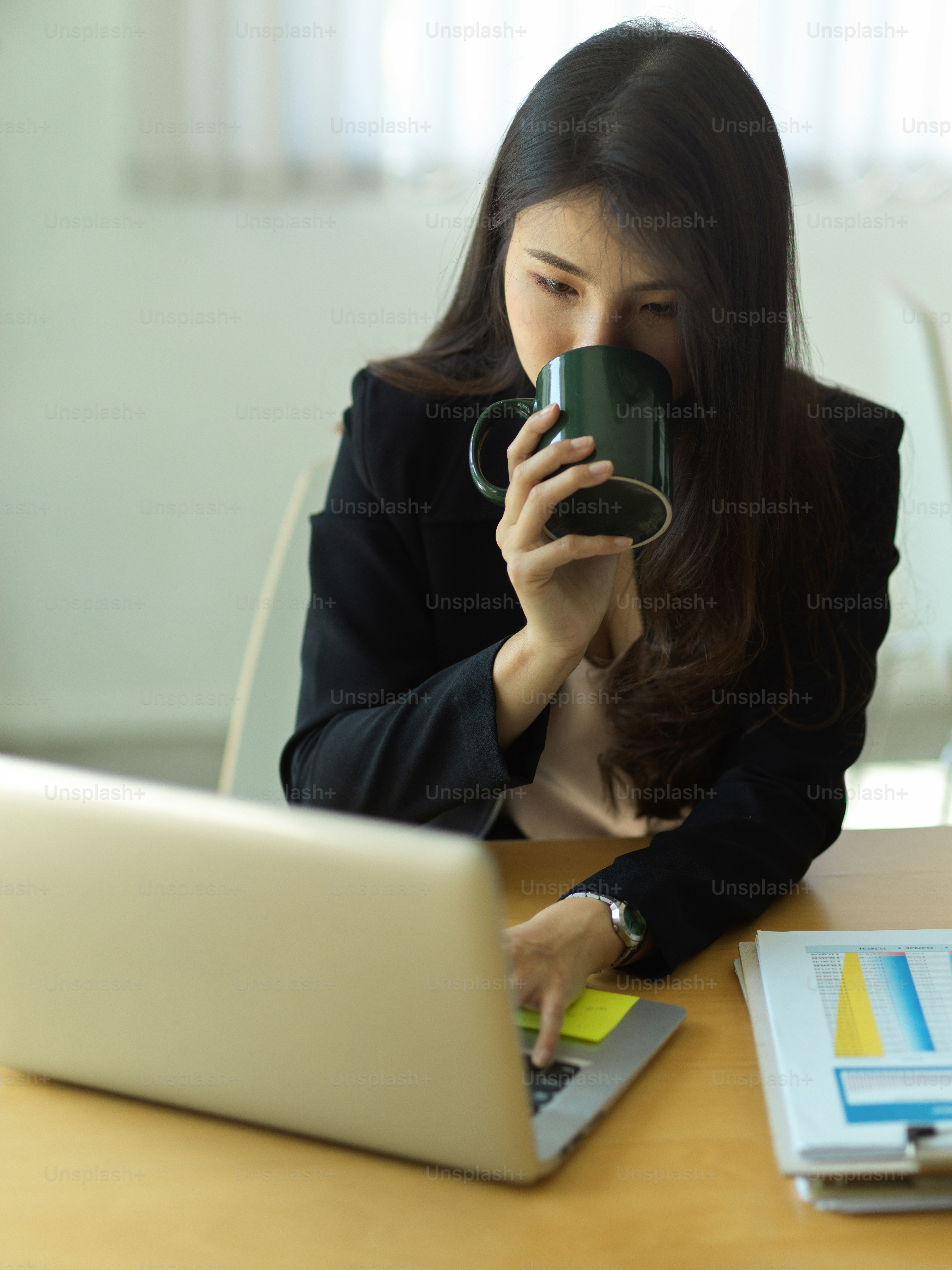 Portrait of young beautiful office worker drinking coffee while working ...
