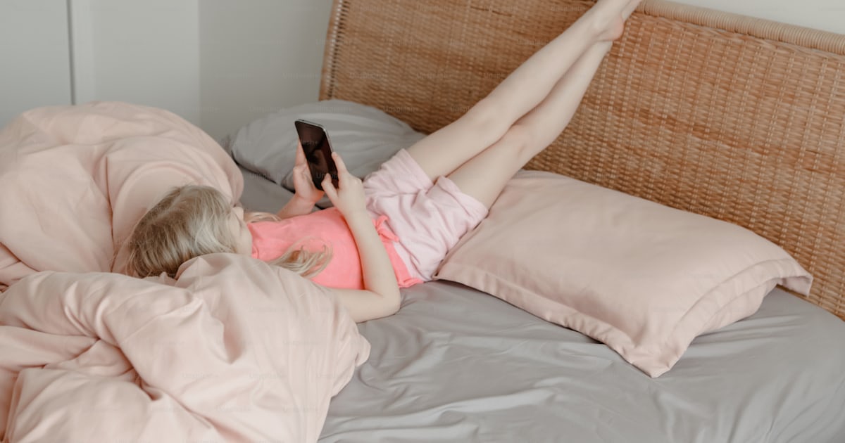 집에서 침대에 누워 온라인으로 스마트폰으로 친구들과 채팅하는 소녀 소셜 미디어에서 전화로 타이핑을 하는 아이 아이 코로나