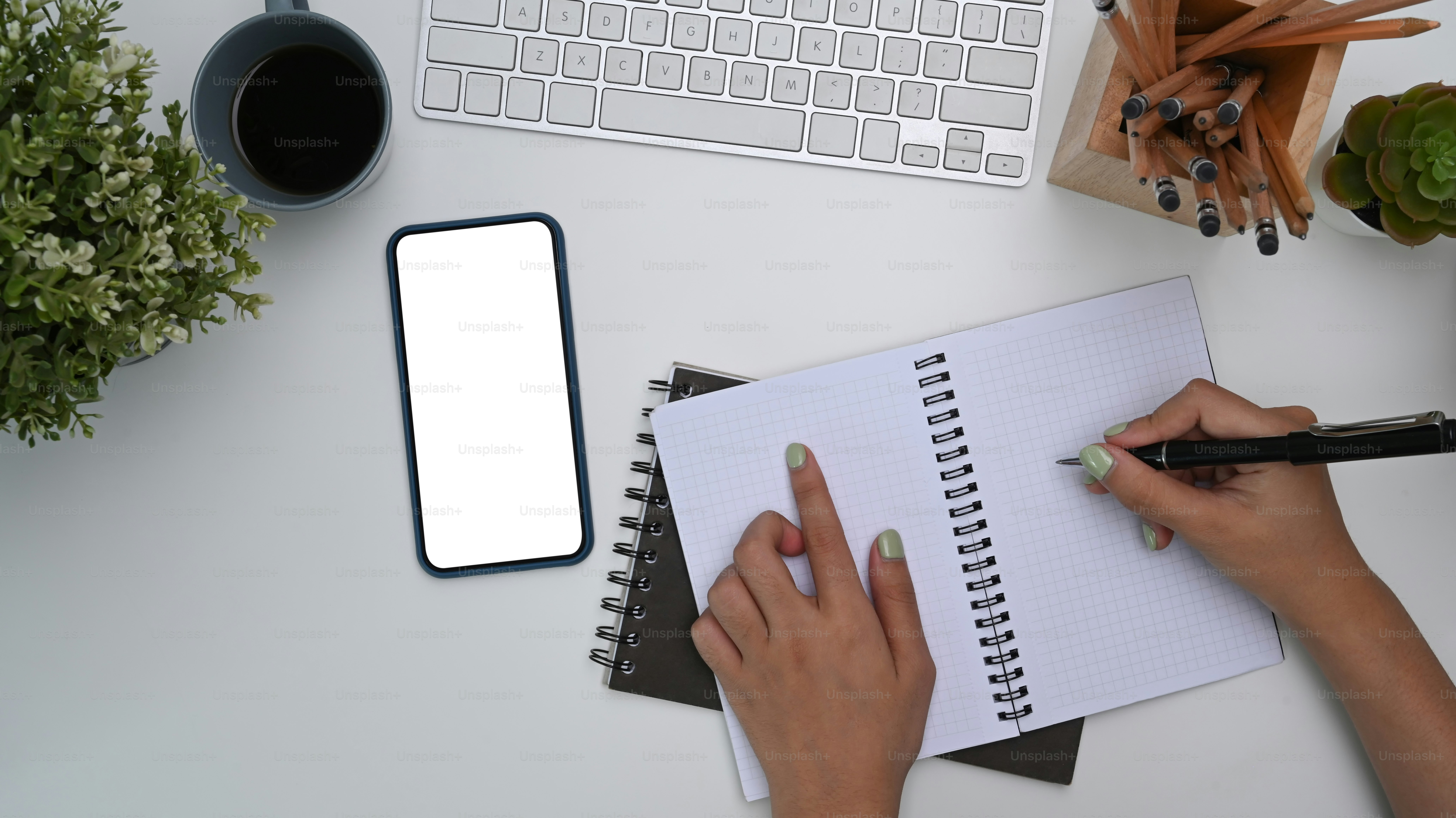 Overhead shot of woman making note on notebook at white office desk ...