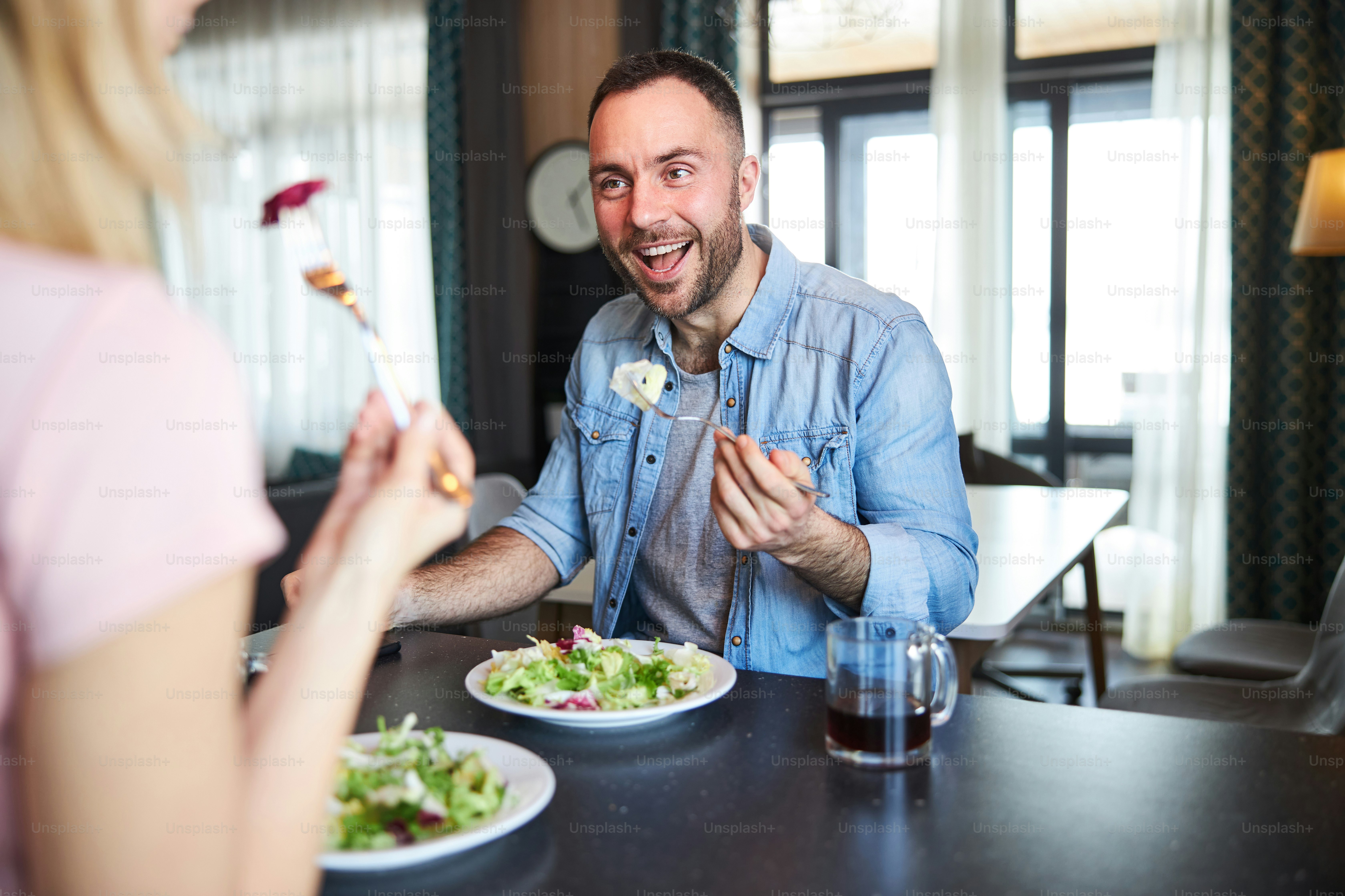 Handsome gentleman eating salad and laughing while sitting at the table ...
