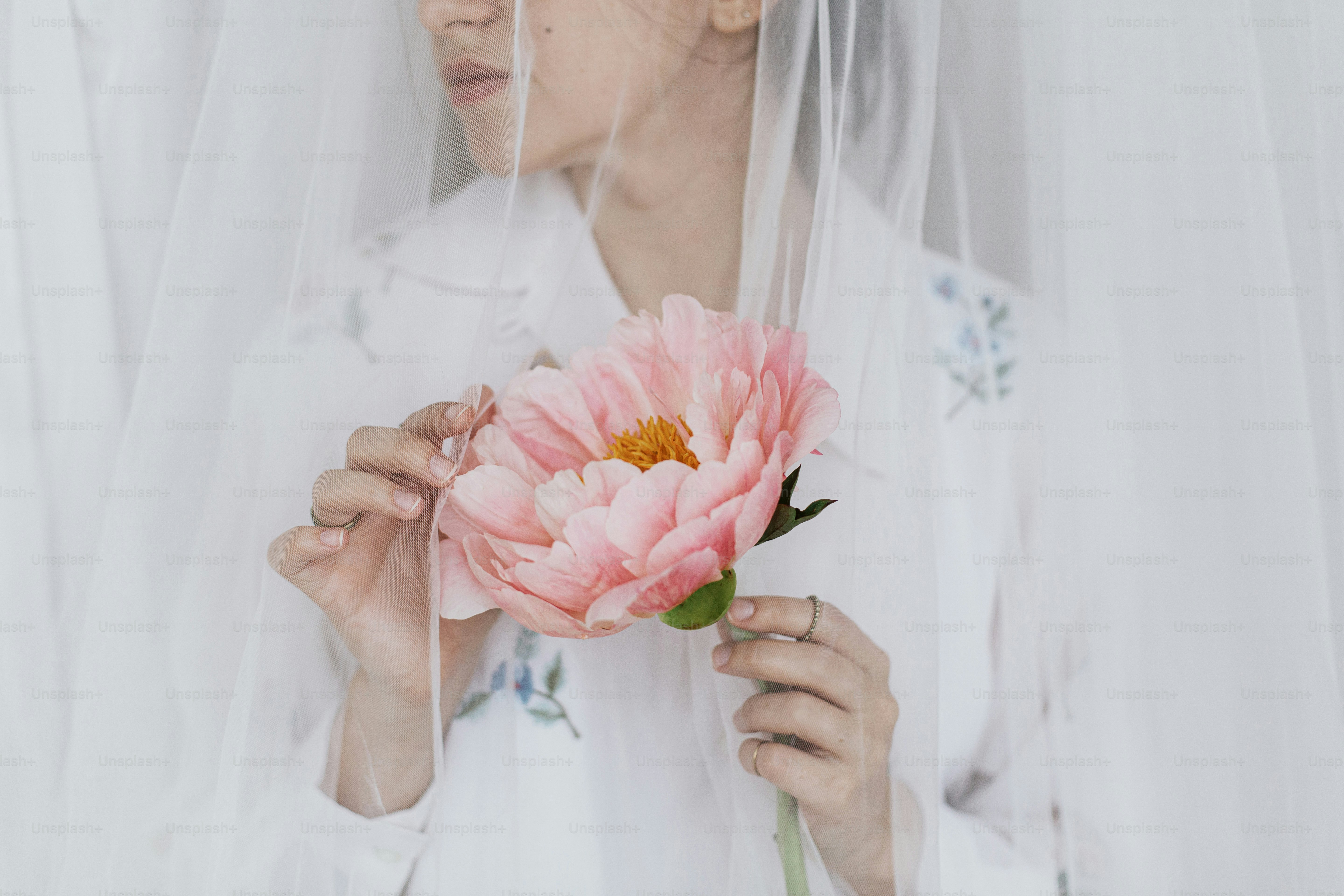 Beautiful stylish woman behind soft white tulle holding peony in hands. Young female gently ...