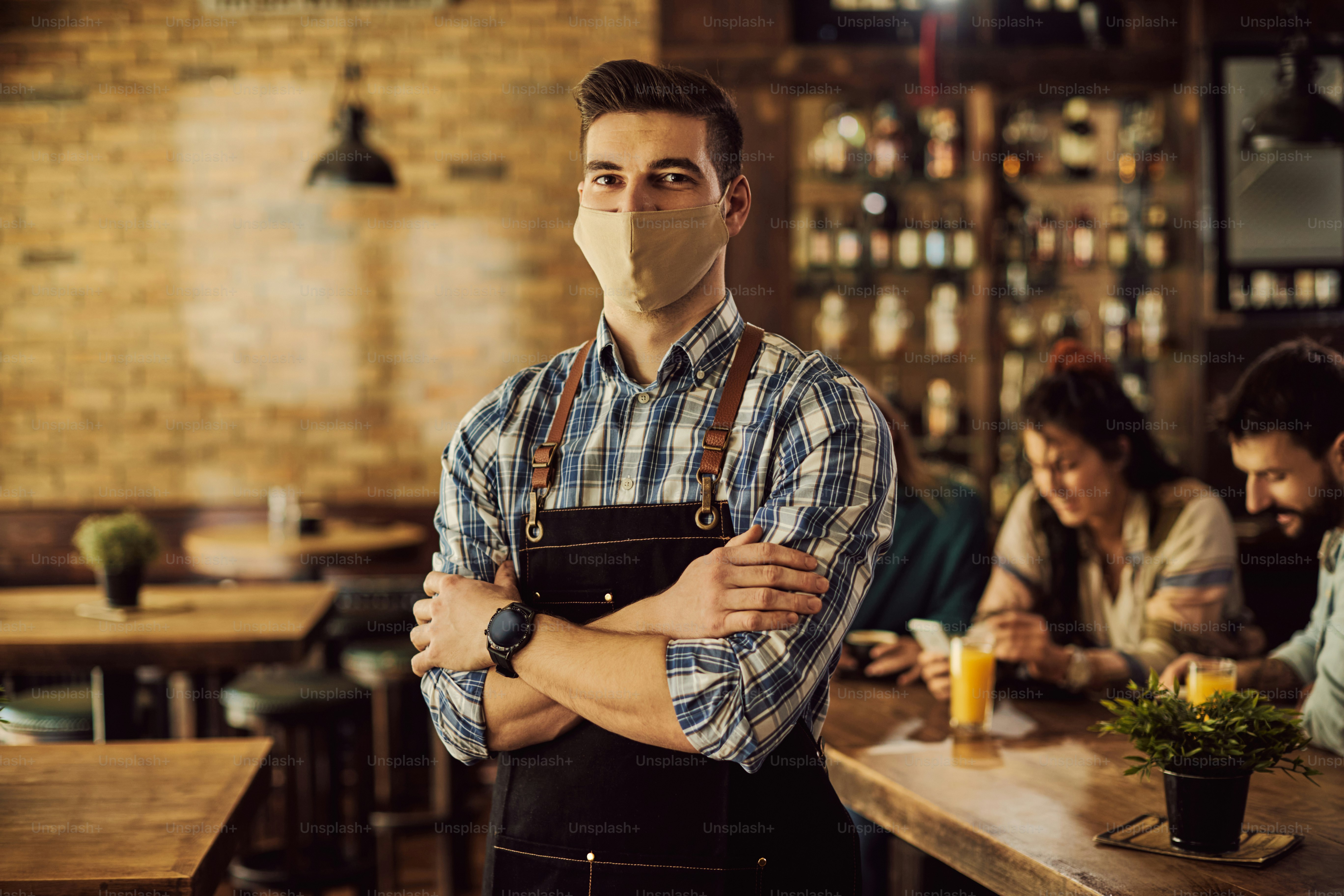 Portrait of waiter wearing protective face mask while standing with ...