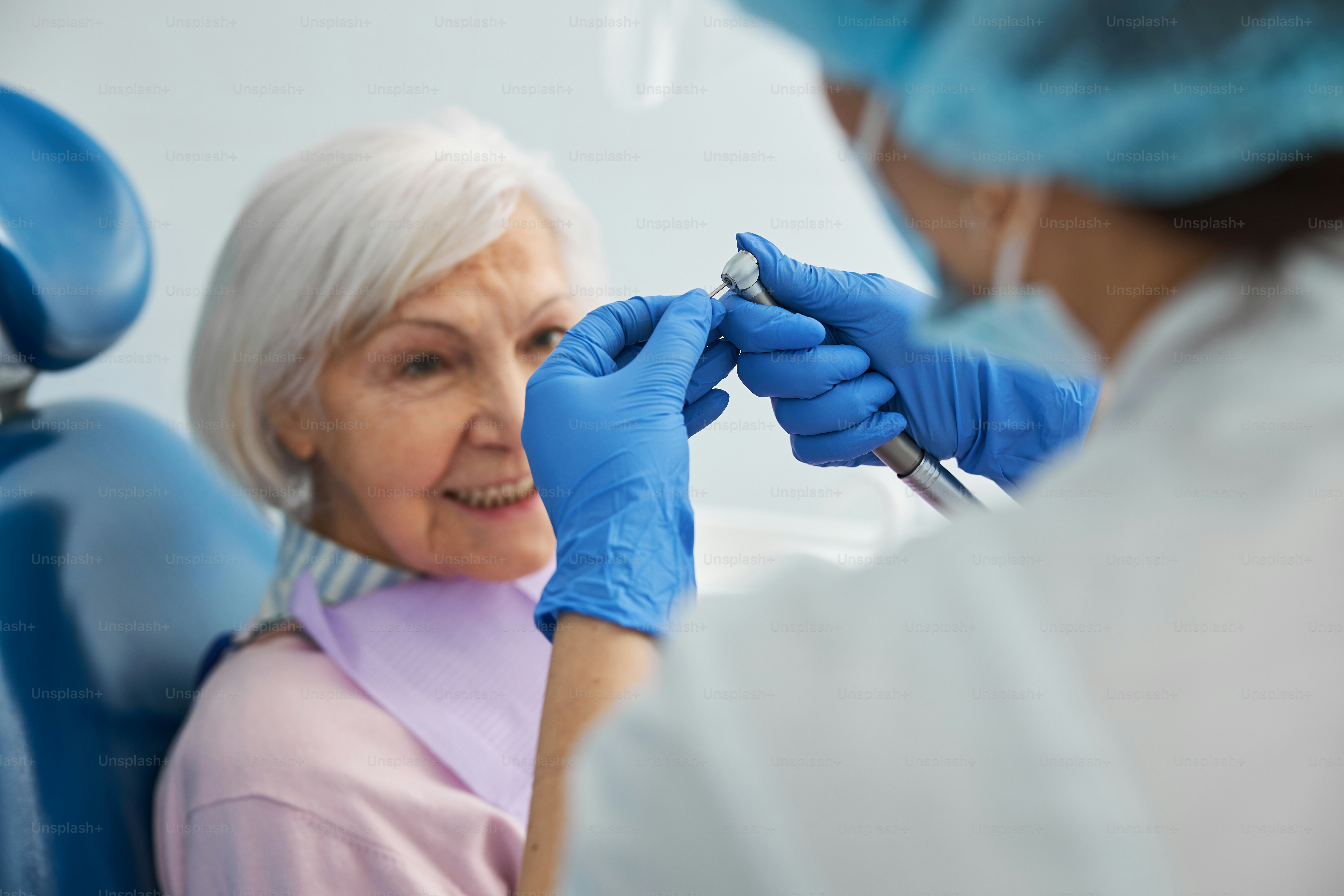 Dental office employee keeping a handpiece in front of lady face while ...