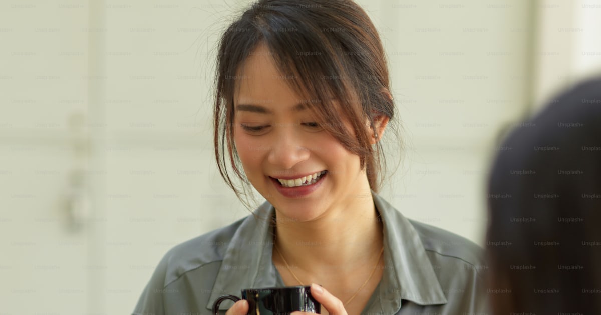 사무실에서 동료의 맞은편에 앉아 컵을 들고 웃고 있는 여성의 크롭 샷 사진 Unsplash의 사진술 이미지