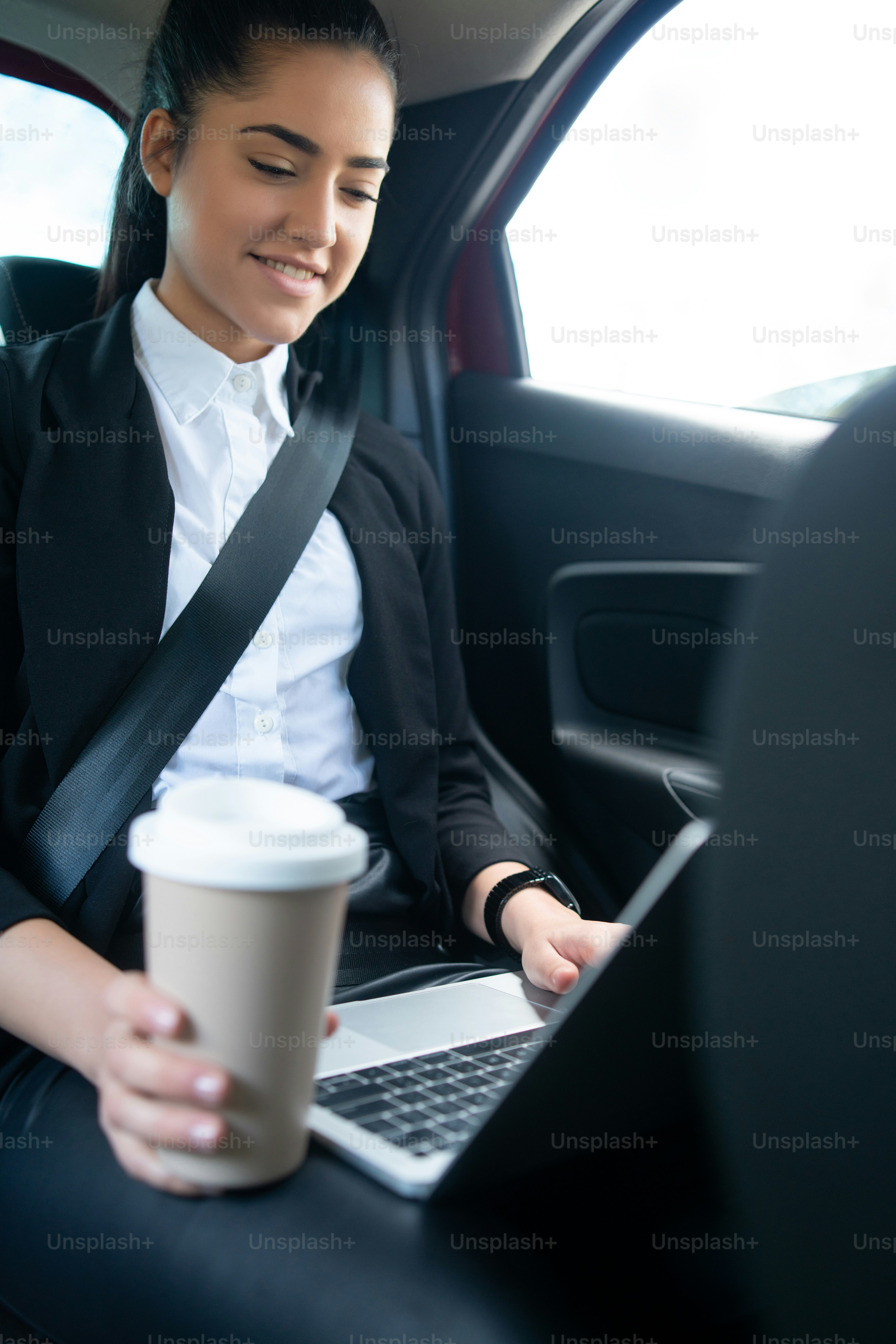 Portrait of business woman using her laptop on way to work in a car ...