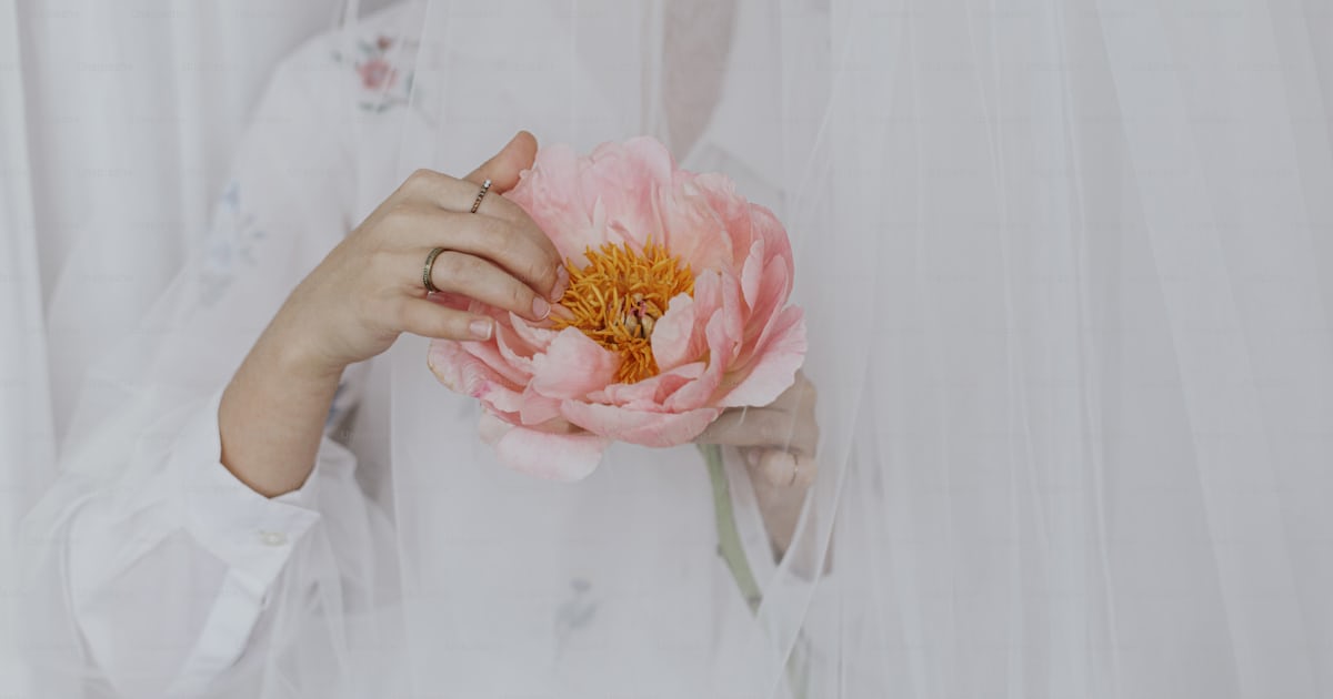 부드러운 흰색 얇은 명주 그물 뒤에 아름 다운 세련 된 여자는 손에 모란을 들고 있습니다 젊은 여성은 부드럽게 큰 분홍색 모란