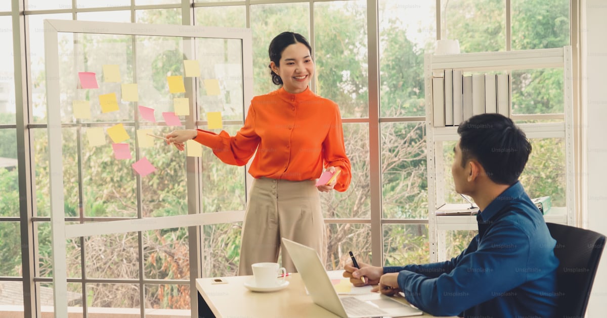 비즈니스 사람들은 사무실의 프로젝트 계획 보드에서 일하고 동료 친구와 대화하여 프로젝트 개발을 분석합니다 그들은 유리 벽에