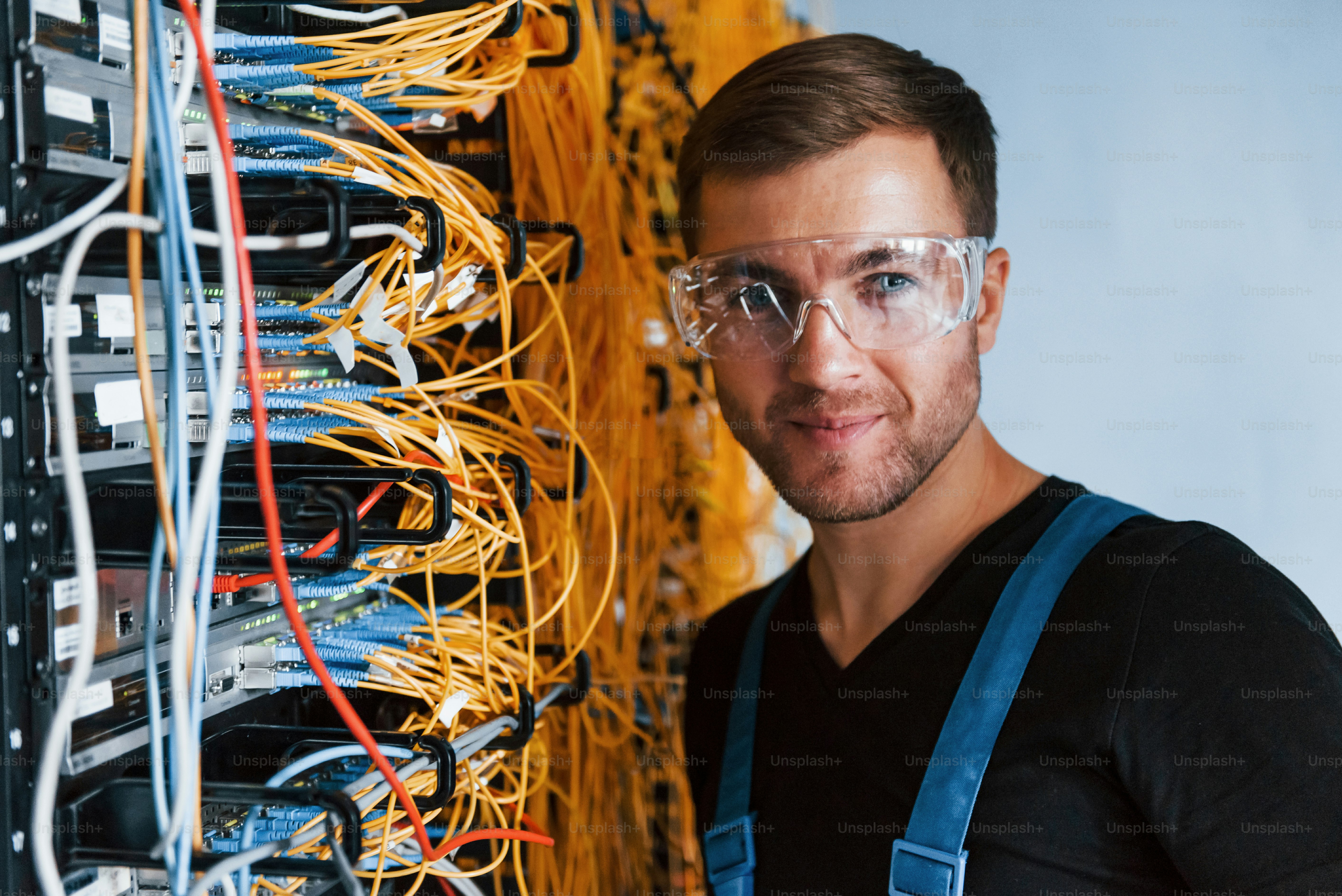 Young man in uniform works with internet equipment and wires in server ...