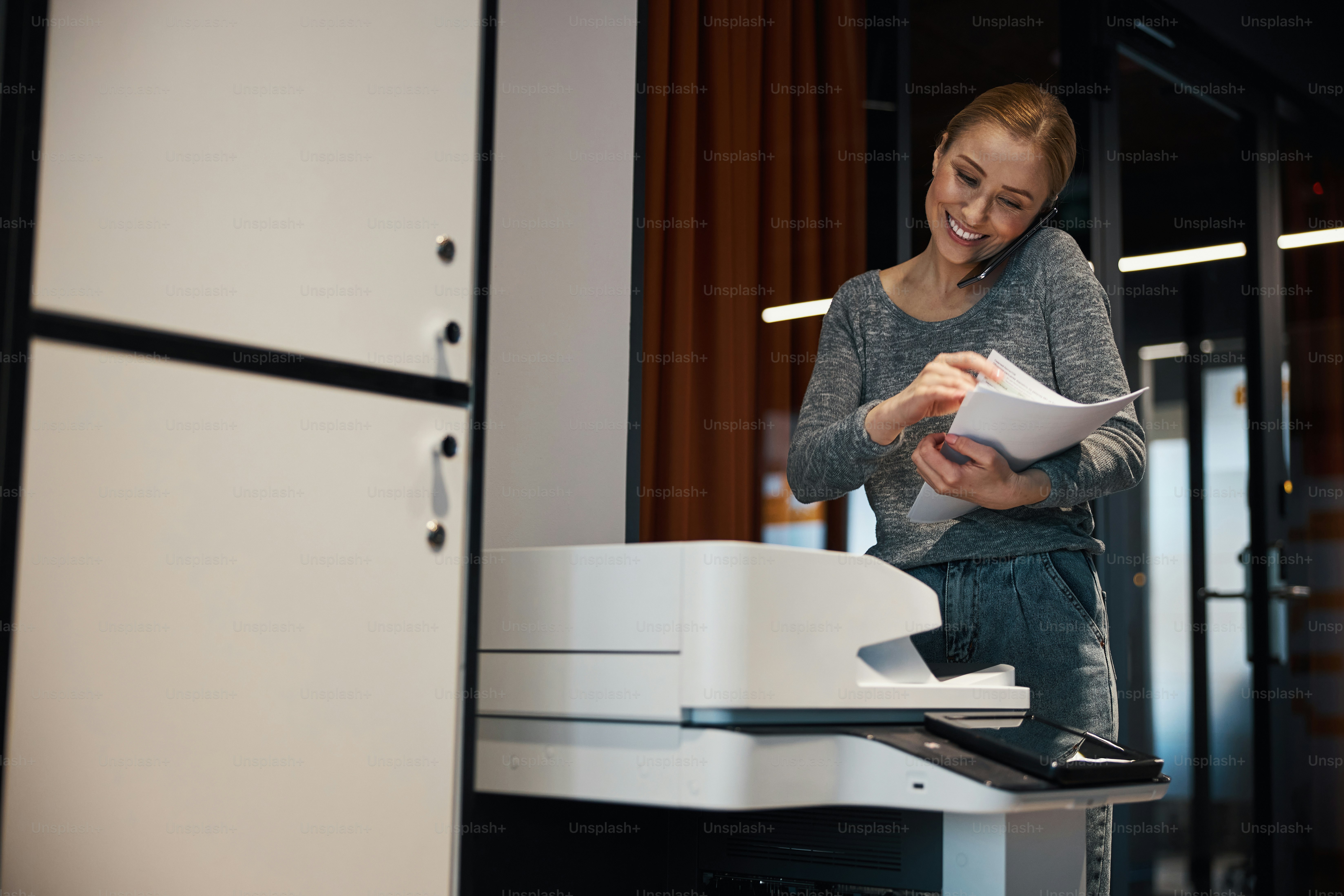 Smiling young blonde woman with a smartphone pressed to the ear ...