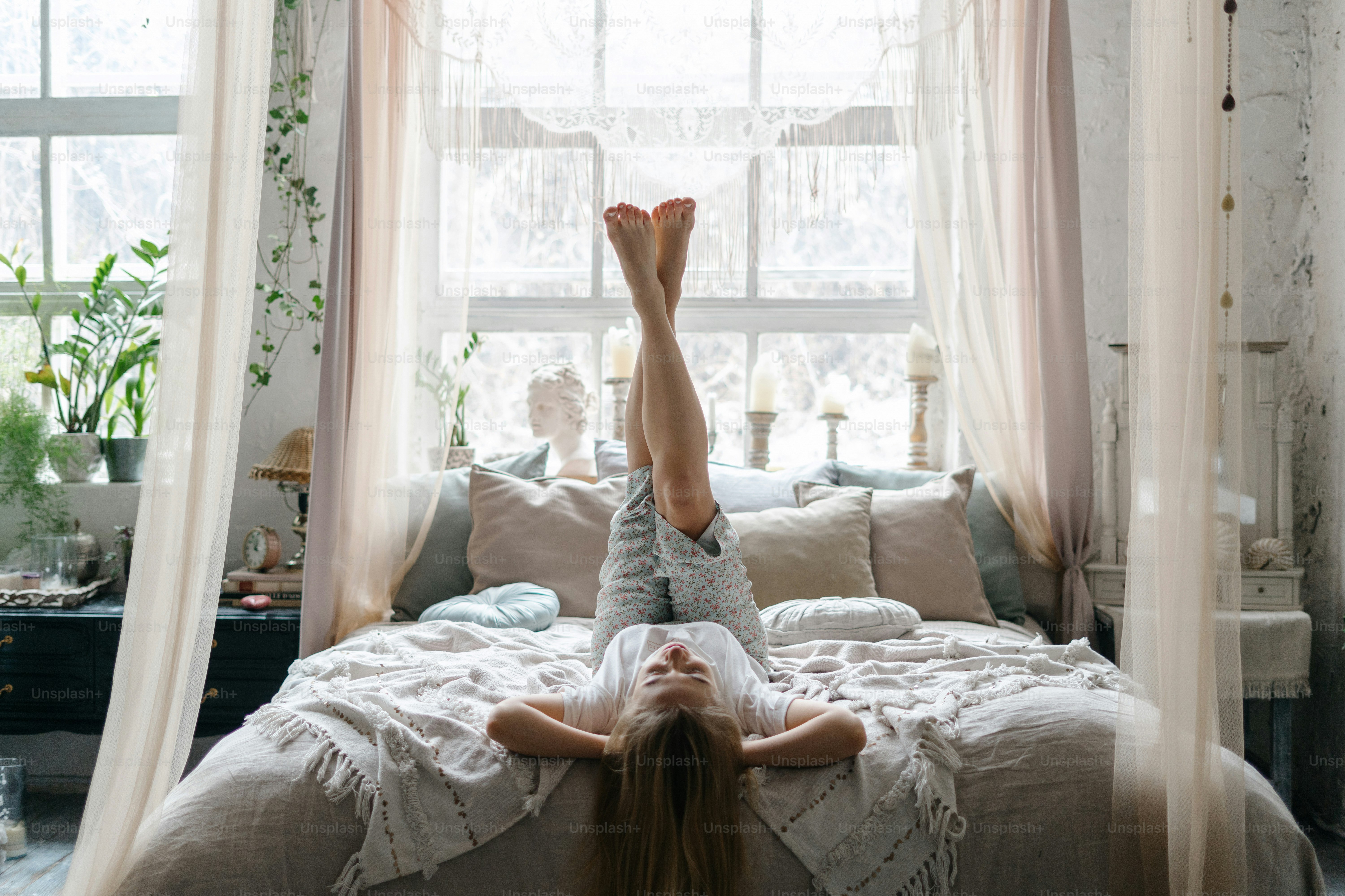 Young woman in sleepwear raised legs up lying on comfortable bed in ...
