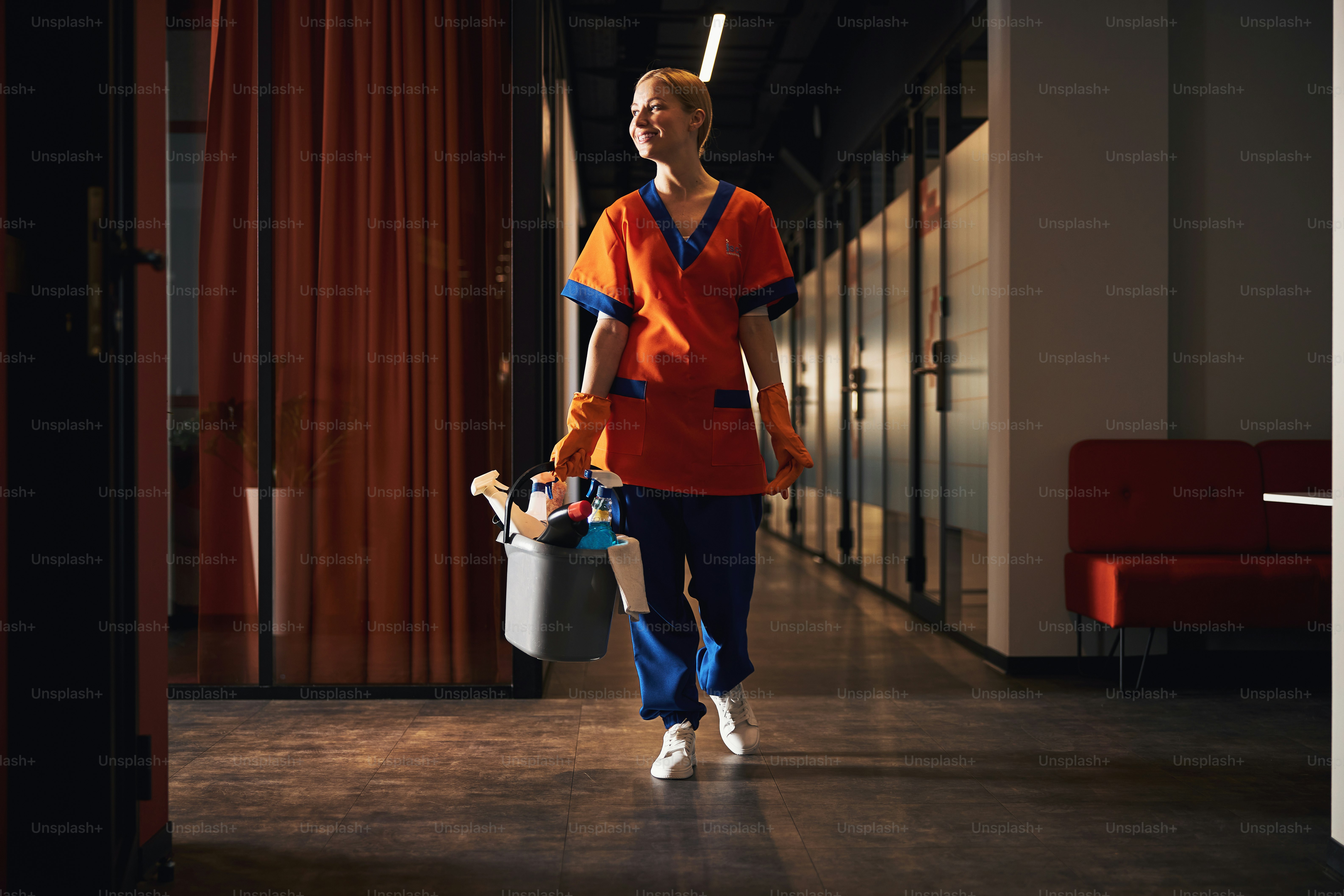 Smiling attractive Caucasian female janitor in rubber gloves carrying a ...