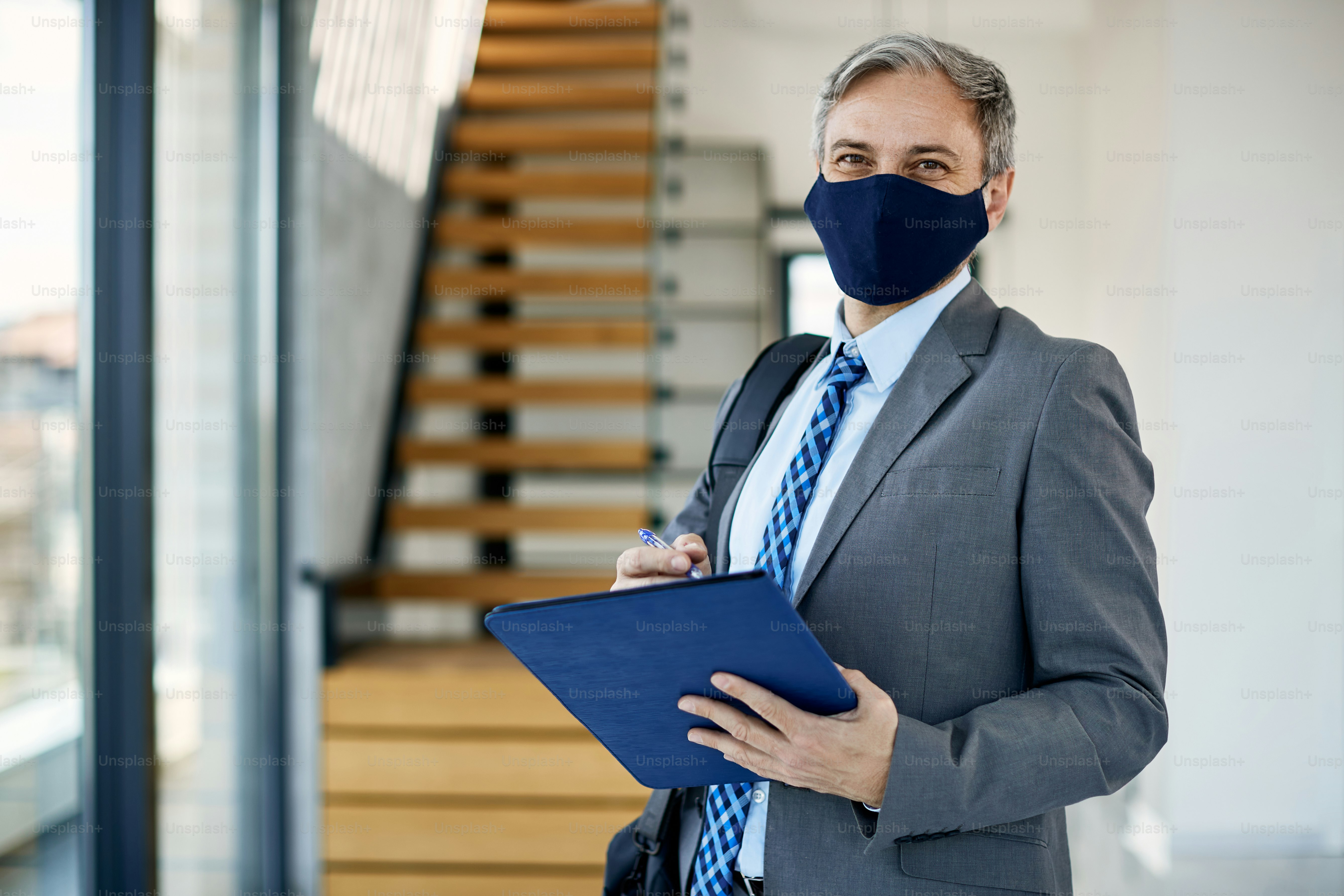 Happy real estate agent with face mask taking notes while checking ...