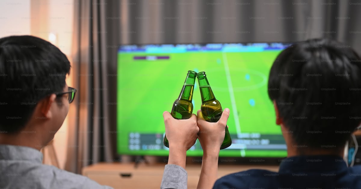 두 남자가 맥주 잔을 부딪치며 소파에서 축구를 응원하는 뒷모습 사진 Unsplash의 축구 팬 이미지