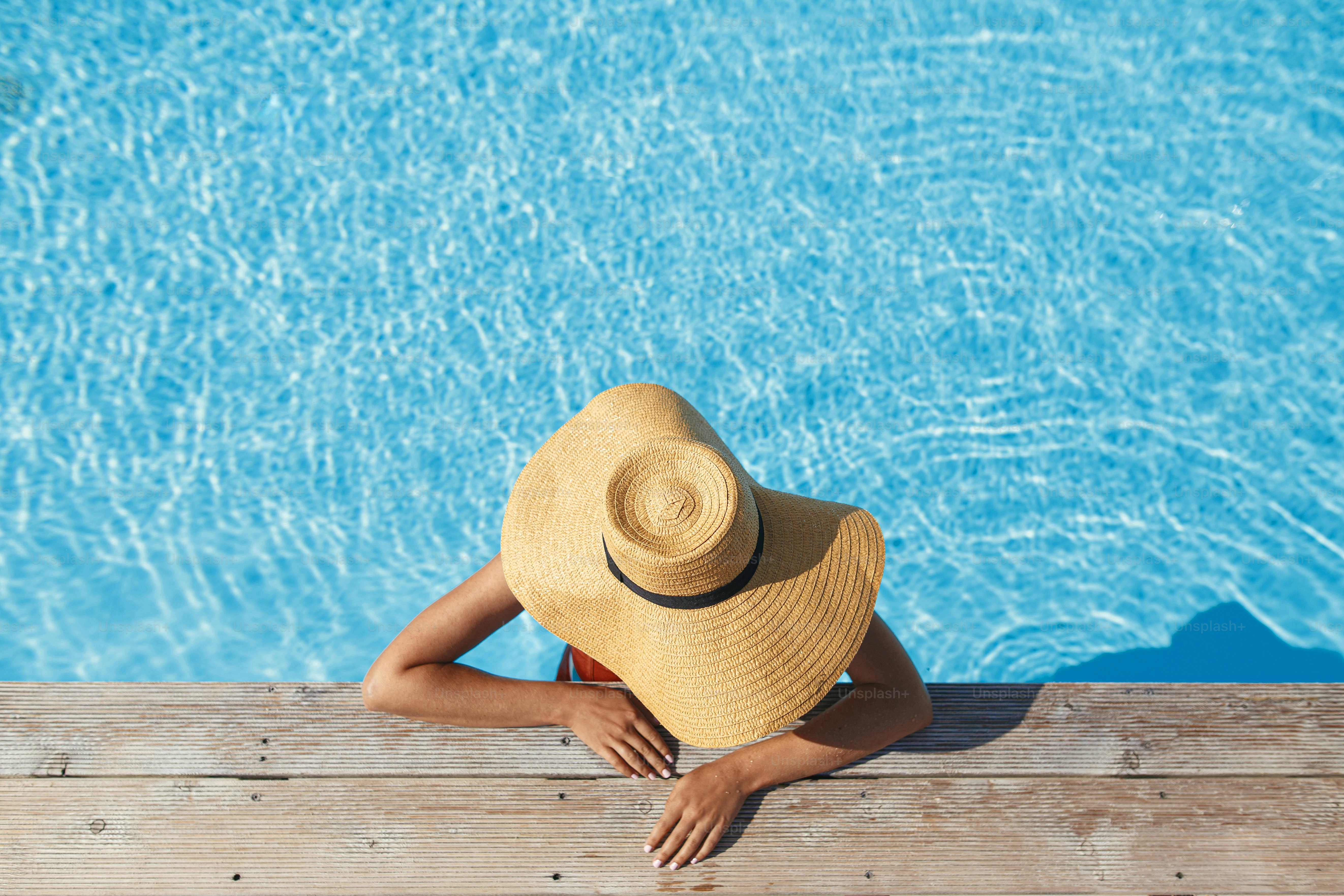 Beautiful woman in hat relaxing under palm leaves shadow on wooden pier ...