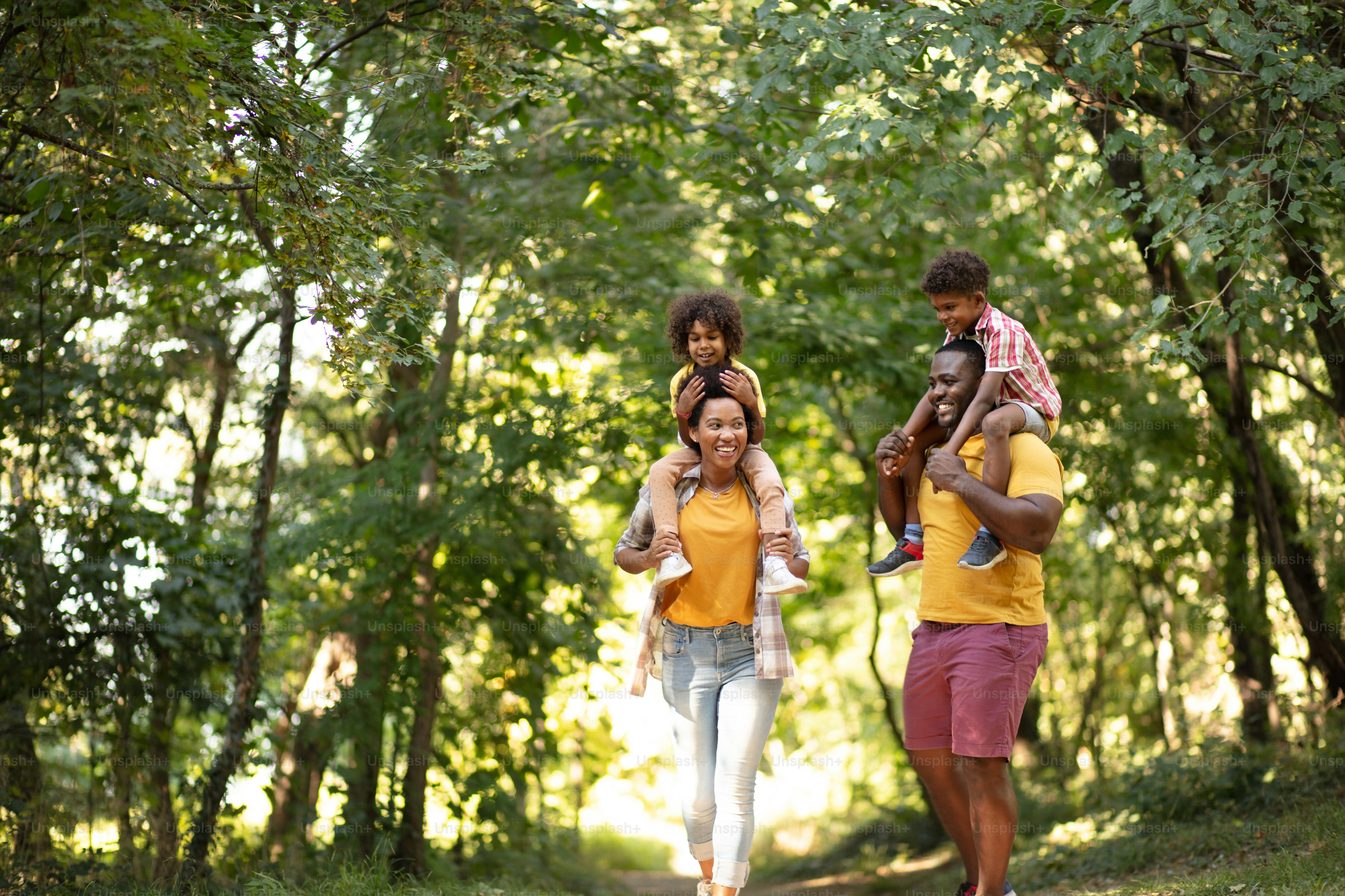 African American family walking trough park. Parents carrying children ...
