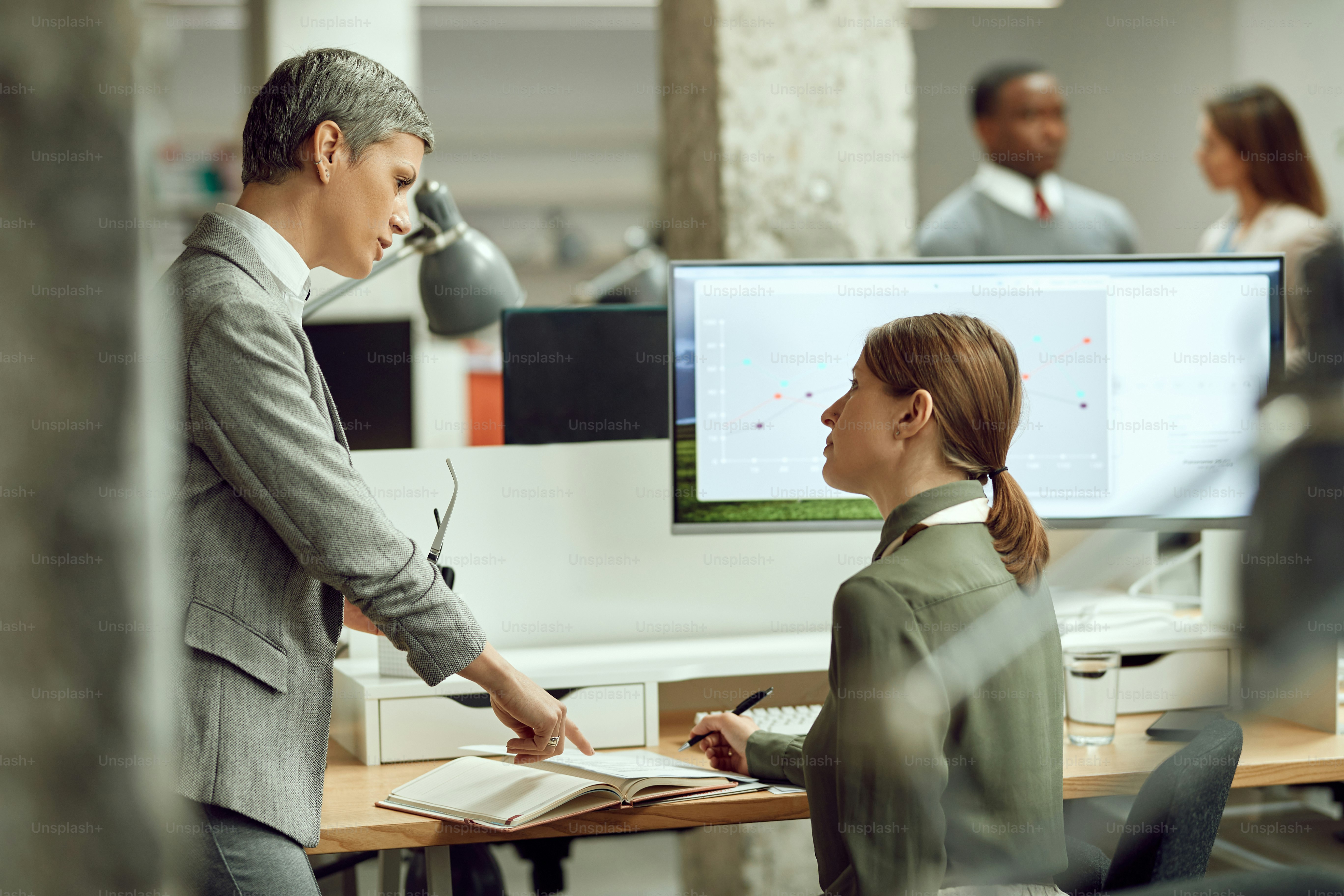 Female CEO assisting colleague with business reports while ...