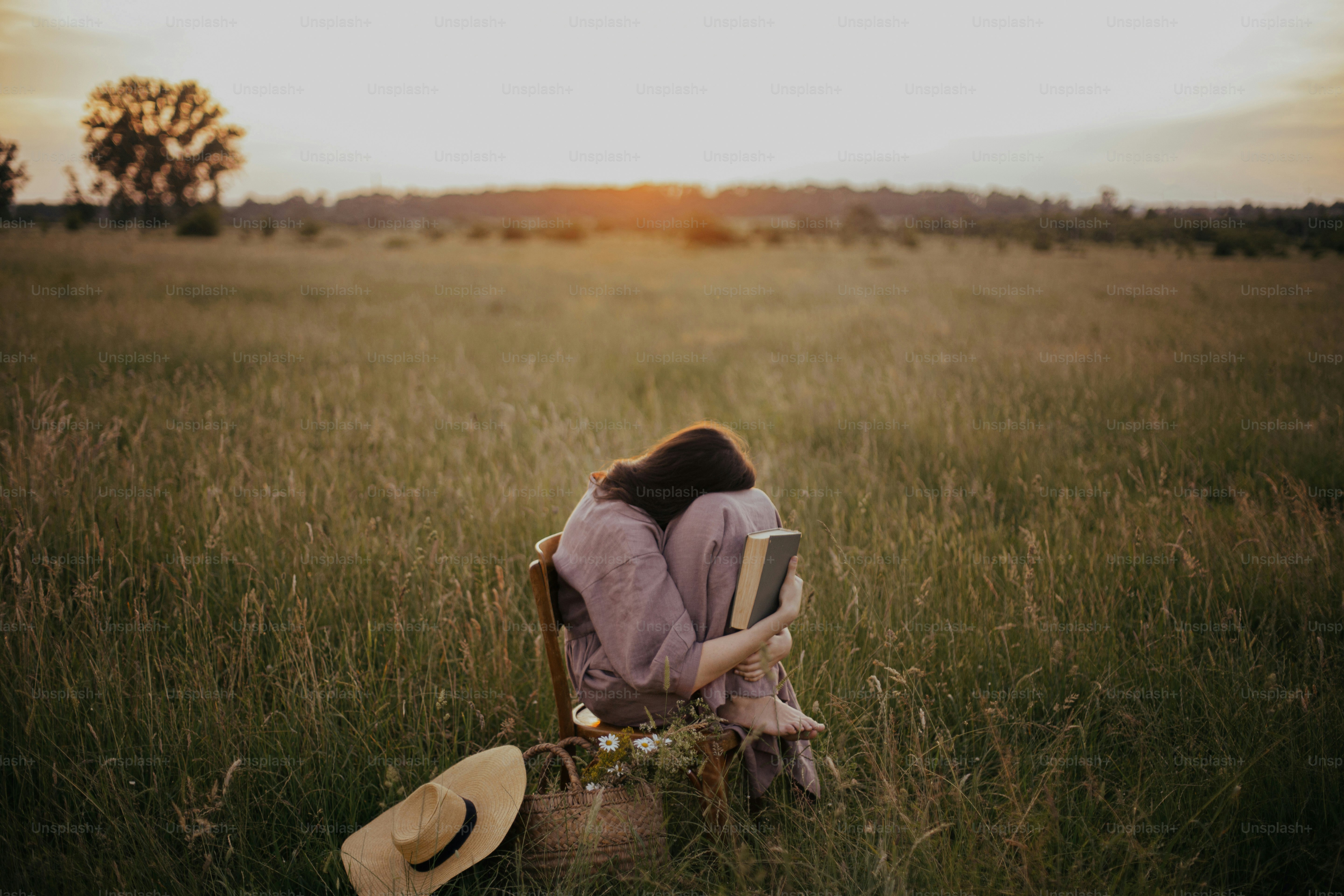 리넨 드레스를 입은 아름다운 여자가 소박한 의자에 앉아 여름 초원에서 꿈을 꾸고 있다 시골 일몰에서 책과 꽃 바구니로 휴식을 취하는 젊은 여성 분위기 있는 고요한 순간