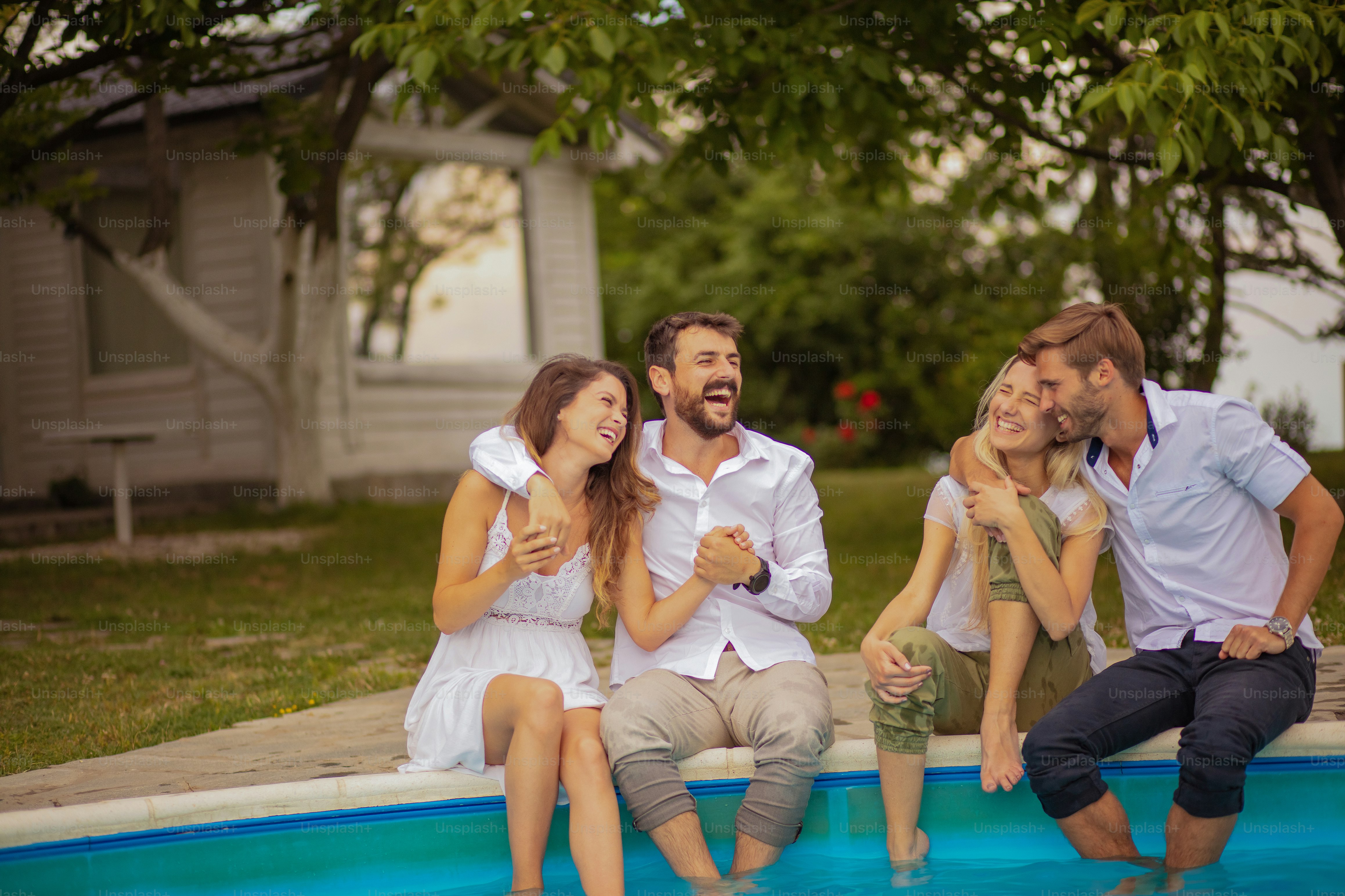 Group of young people sitting on the swimming pool. Day with friends ...
