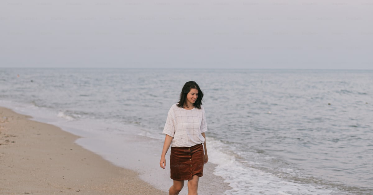 평온한 힙스터 여자는 저녁에 파도가 치는 모래 사장을 맨발로 걷고 고요한 순간을 즐기고 있습니다 캐주얼한 젊은 여성이 리조트의