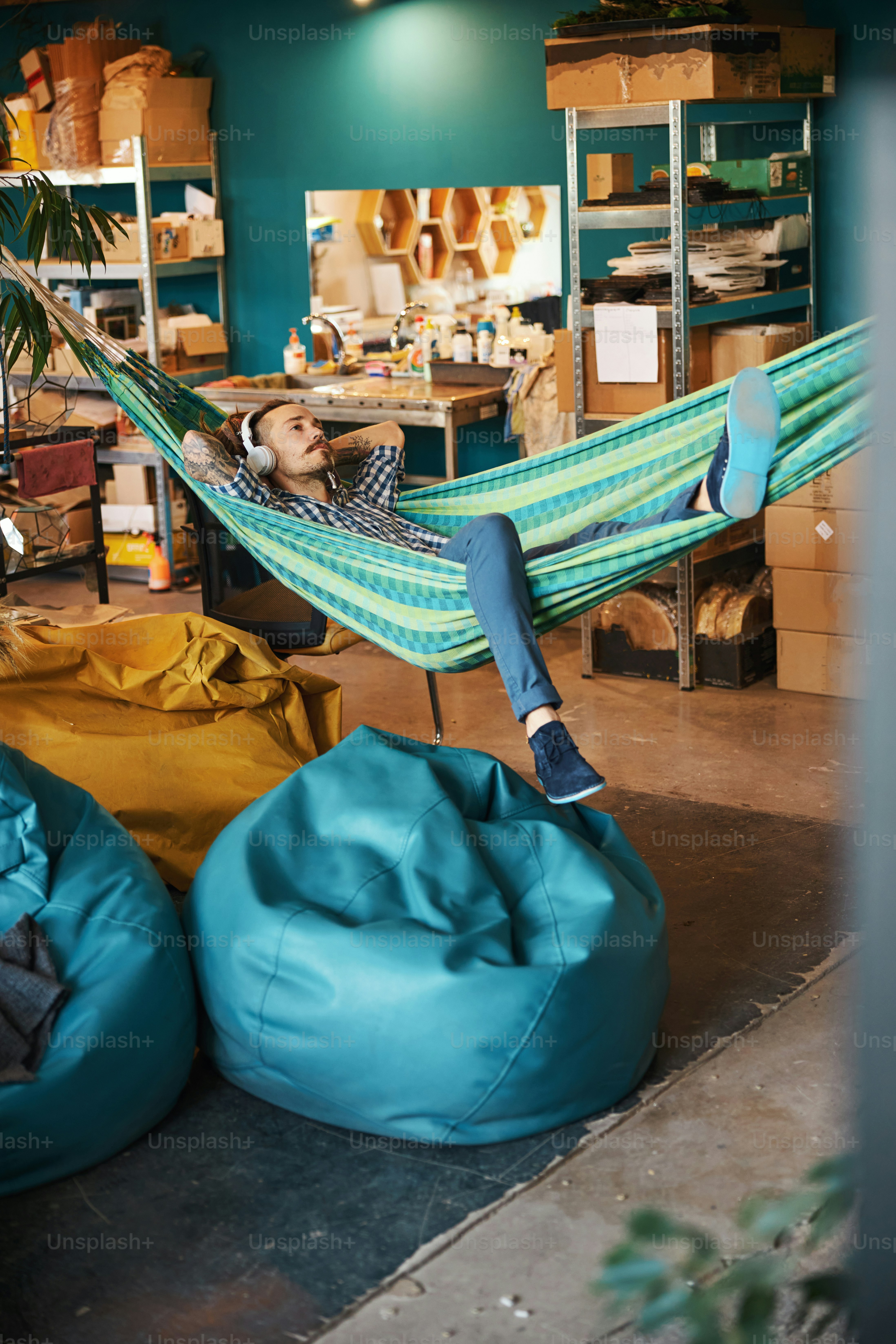 Bearded young man in wireless headphones lying in hammock and enjoying ...