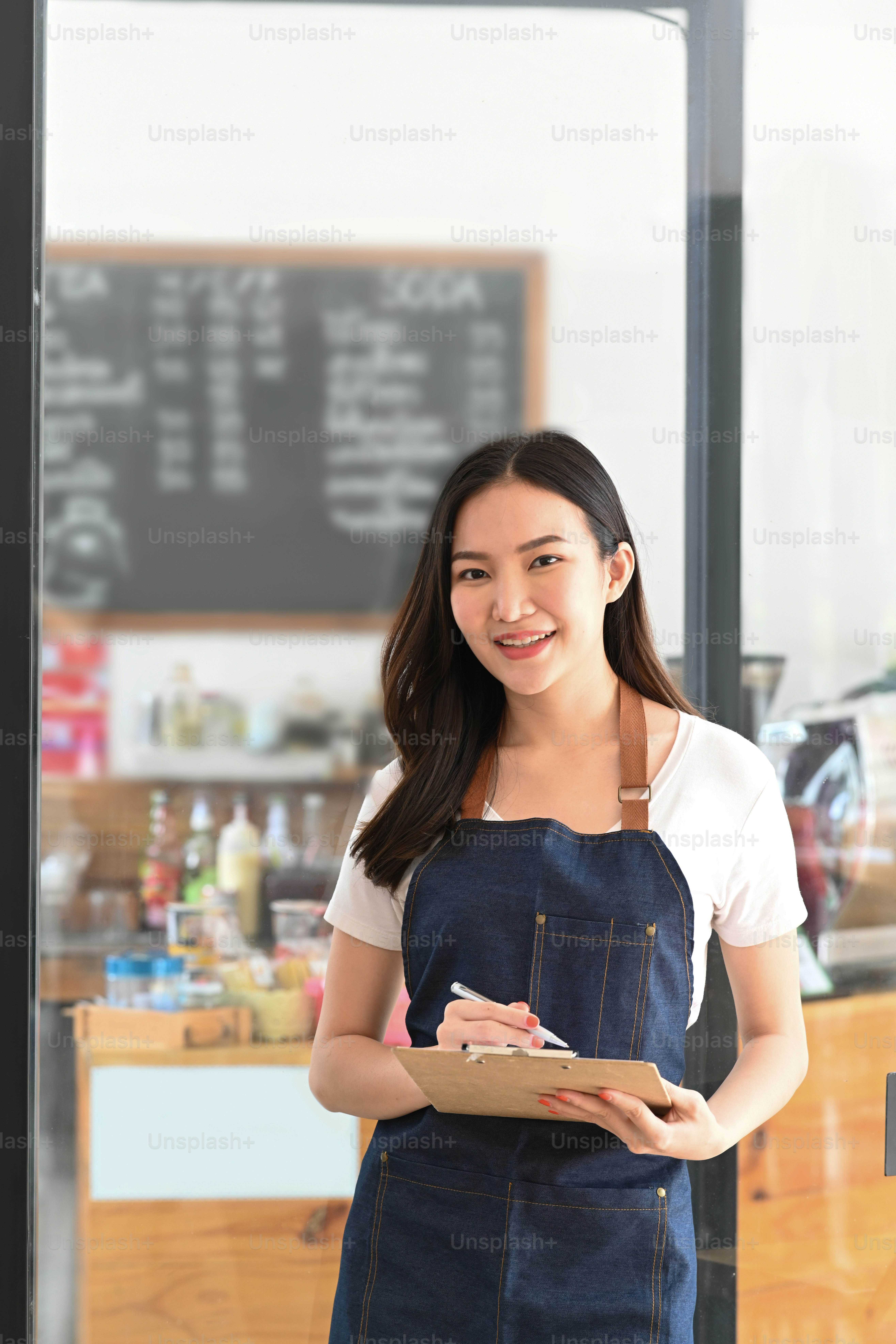 Portrait of friendly waitress holding notepad and smiling to camera ...