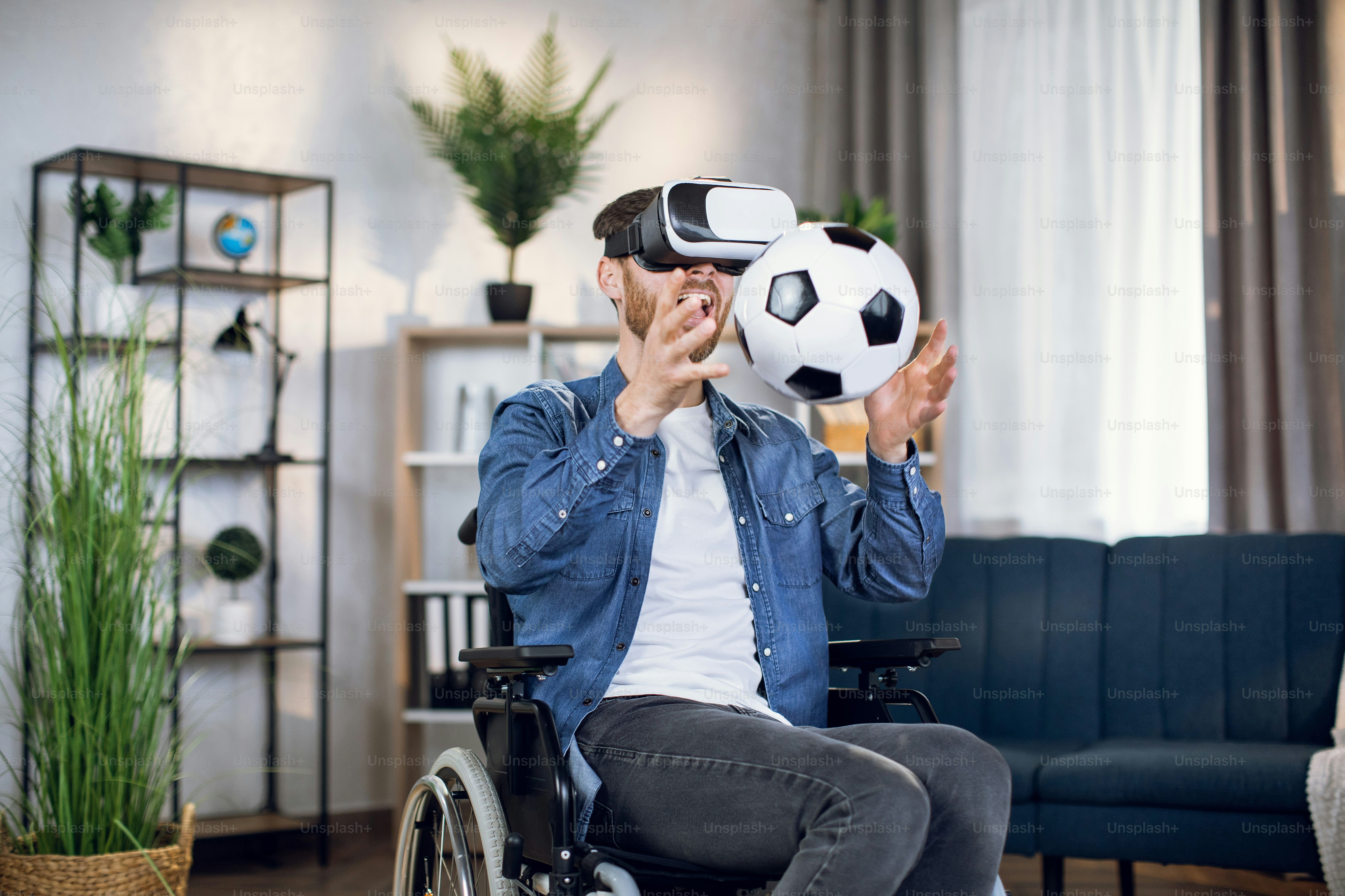 Cheerful young guy sitting in wheelchair using virtual headset for ...
