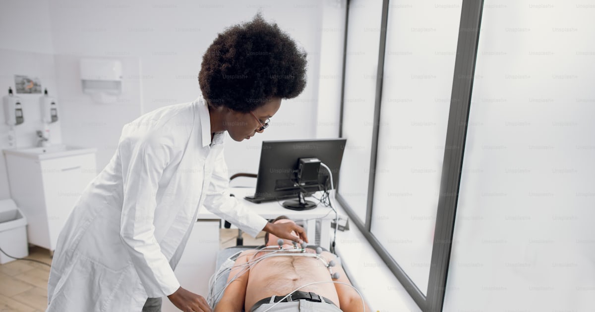 현대 클리닉에서 청년의 Ecg 테스트 젊은 아프리카 여자 의사 심장 전문의는 Ecg를 만들기 전에 남성 백인 환자의 가슴에